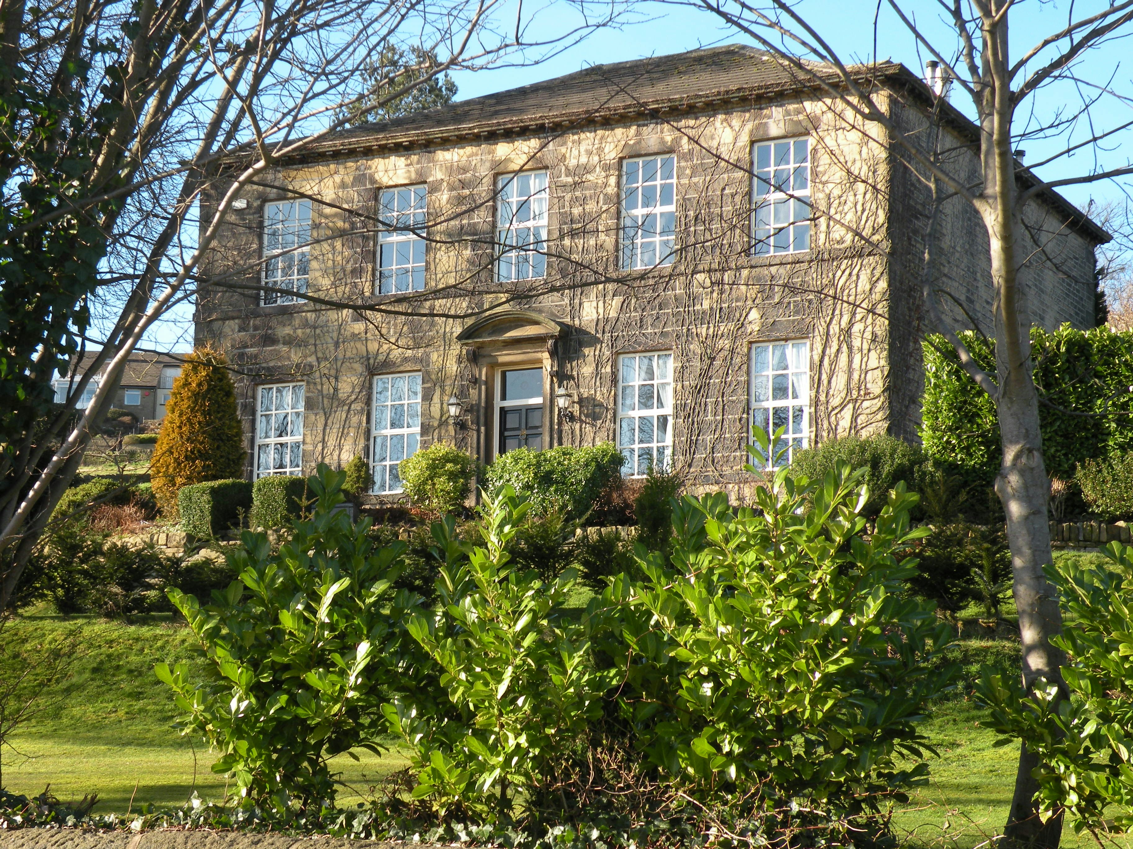 Large stone house with many windows and greenery.