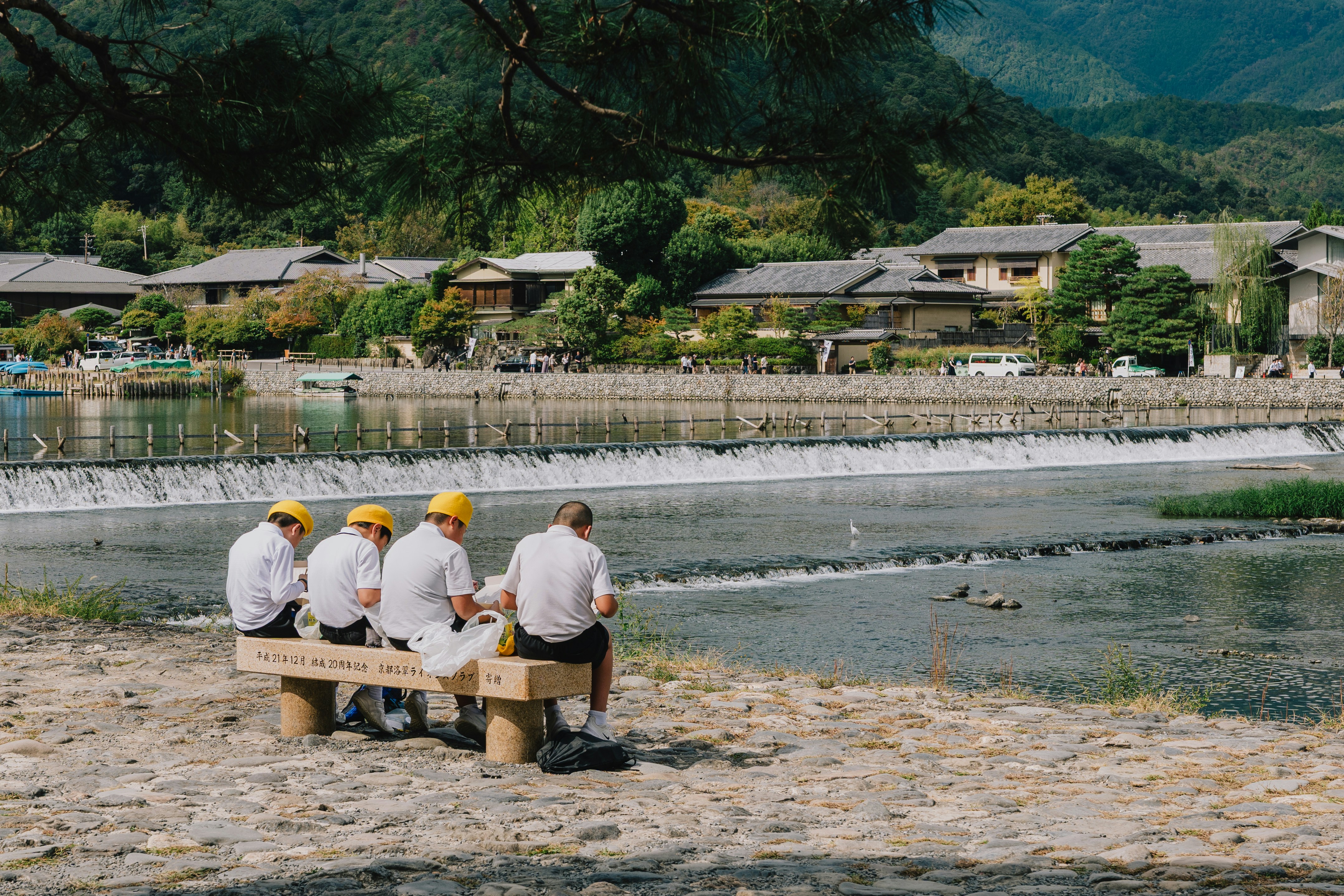 Riverside Pause: Four Workers in Yellow Helmets Rest by the Quiet Riverbank