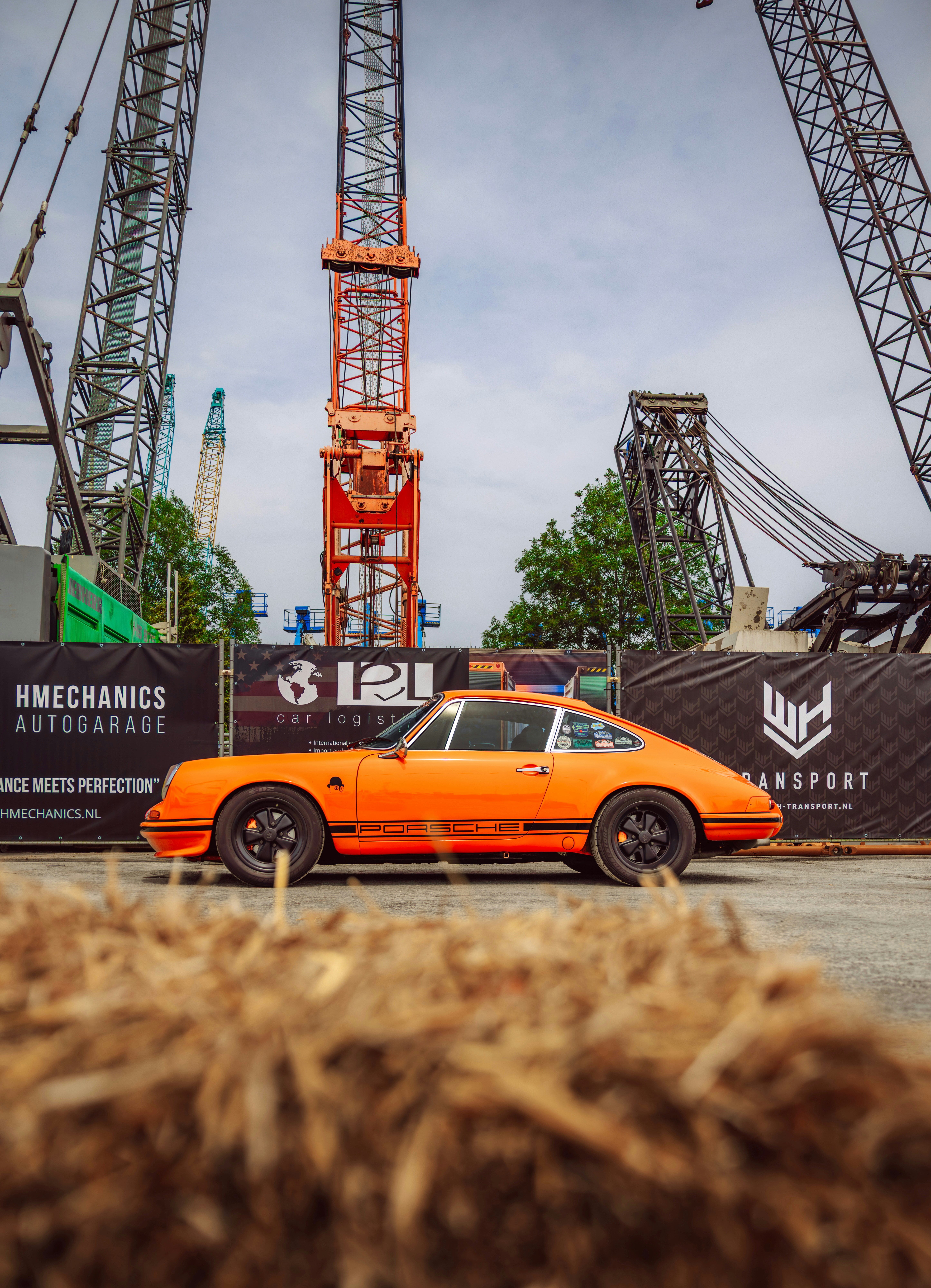 Orange Porsche 911 Anchored Between Towering Cranes