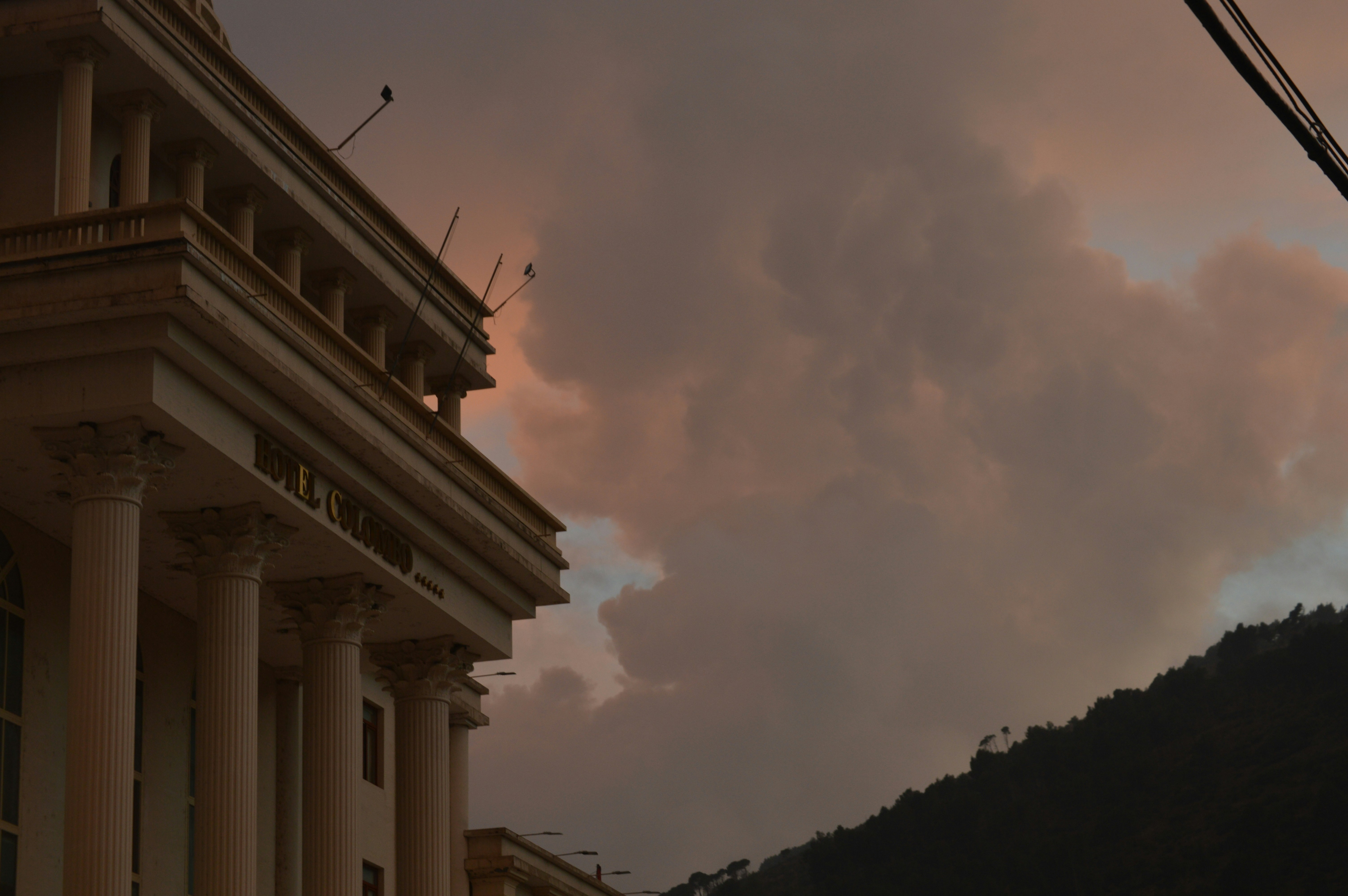 Columns at Dusk: Coral Clouds and a Quiet Hillside Silhouette
