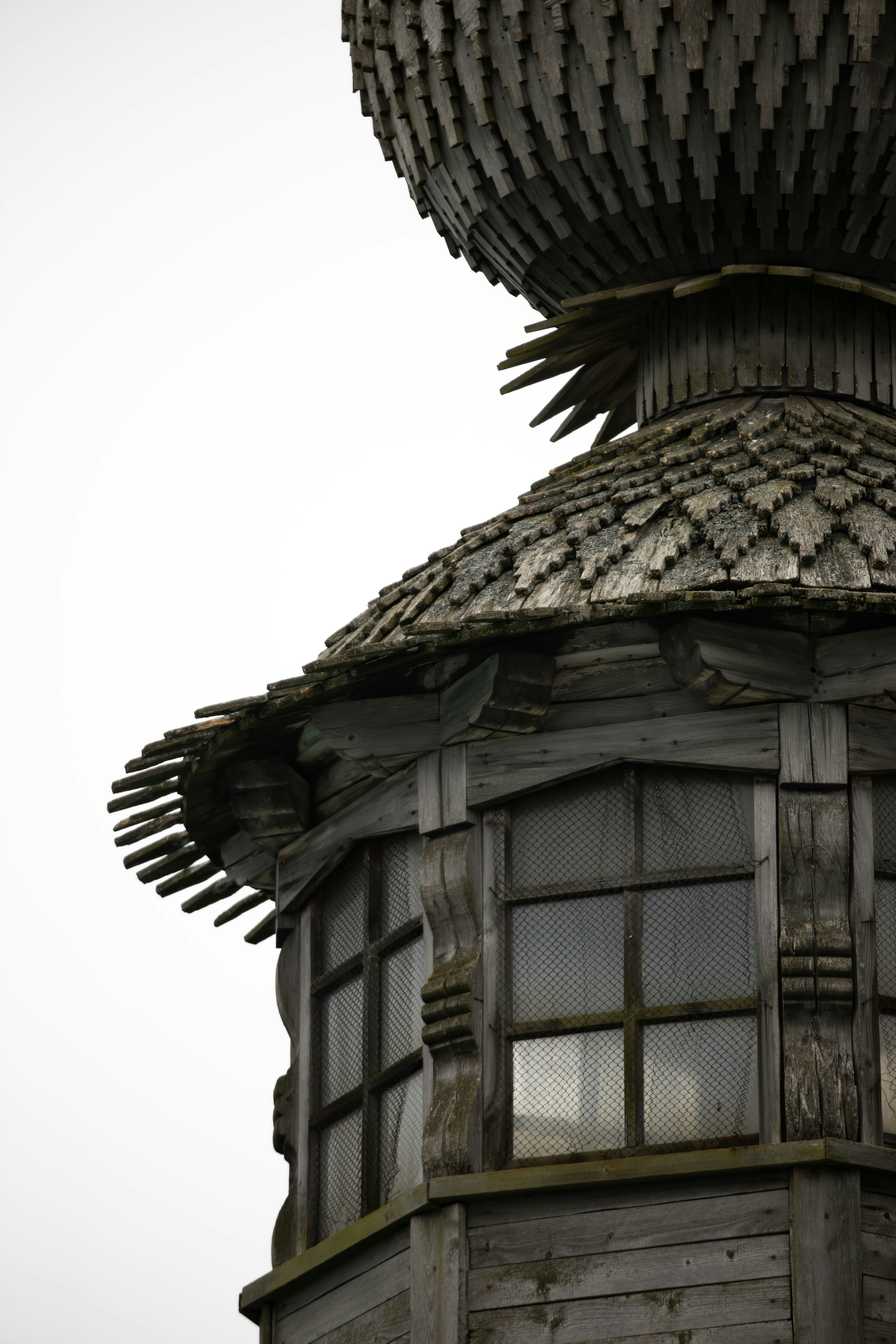 Weathered wooden turret with a multi-tier shingled roof and lattice-pane windows rises against a pale sky.