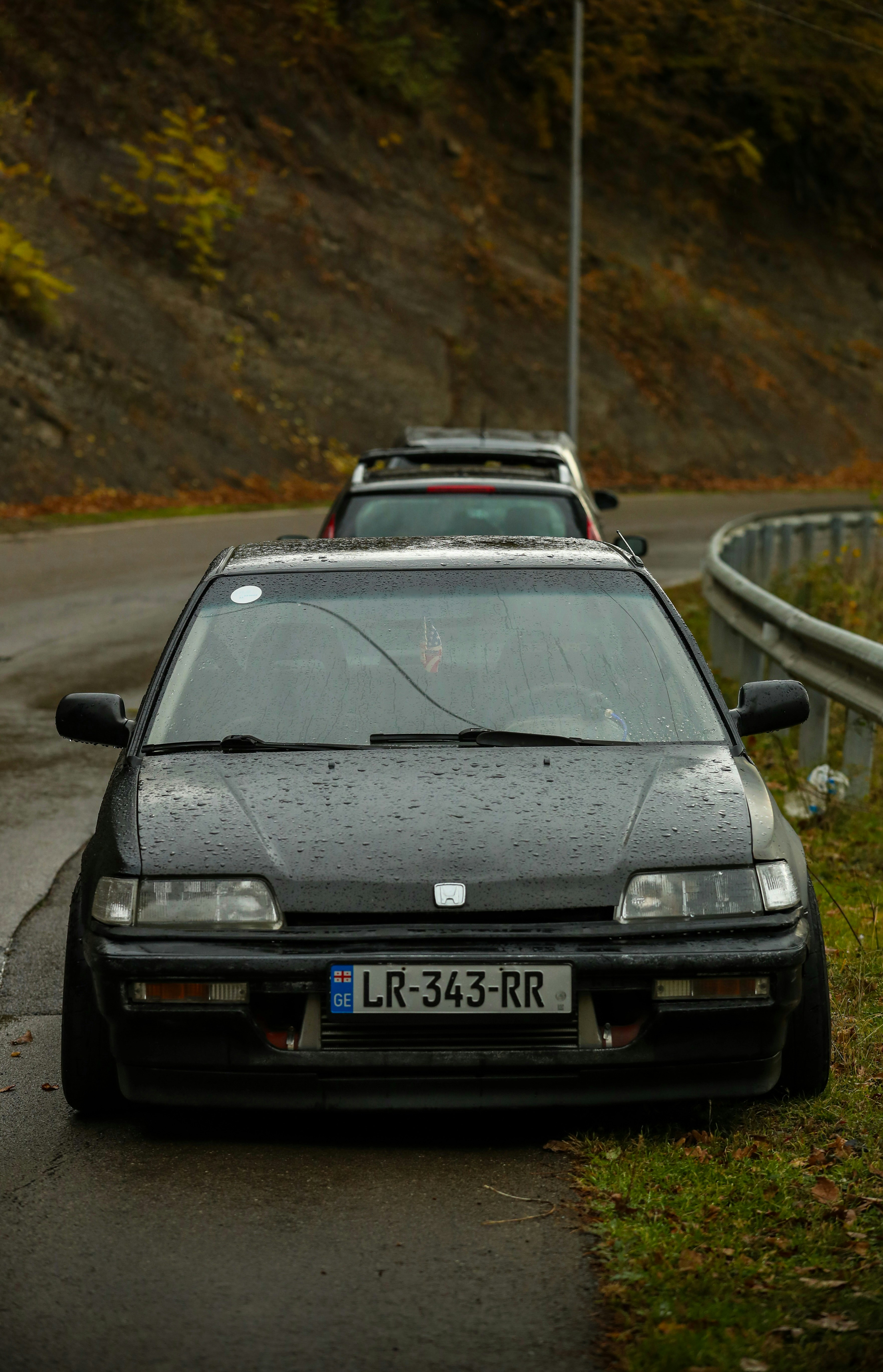 Rain-Washed Front Car Leads a Line on a Winding Autumn Road