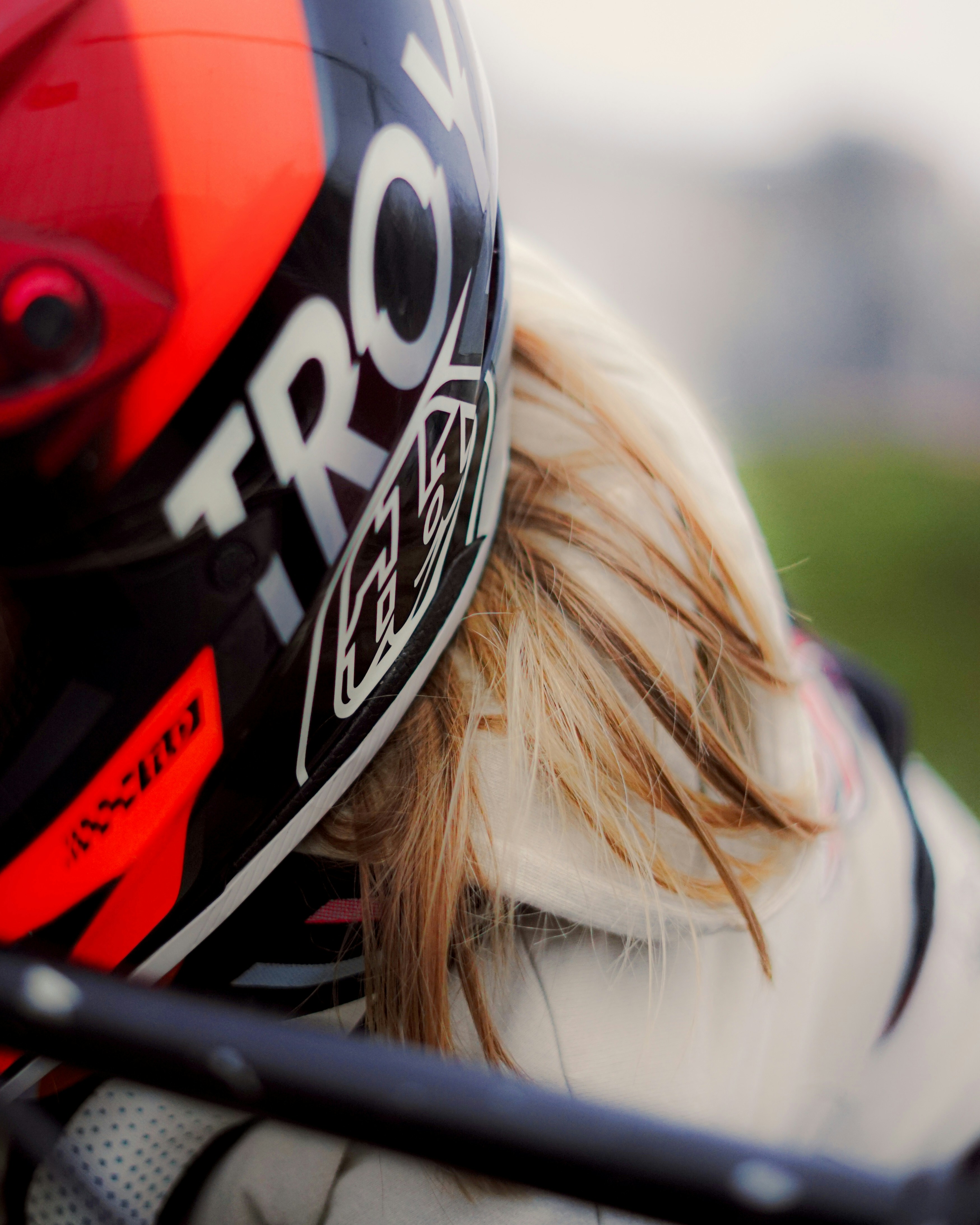 Close-Up on a Racing Helmet: Red Shell, Bold Logos, and Wind-Chased Blonde