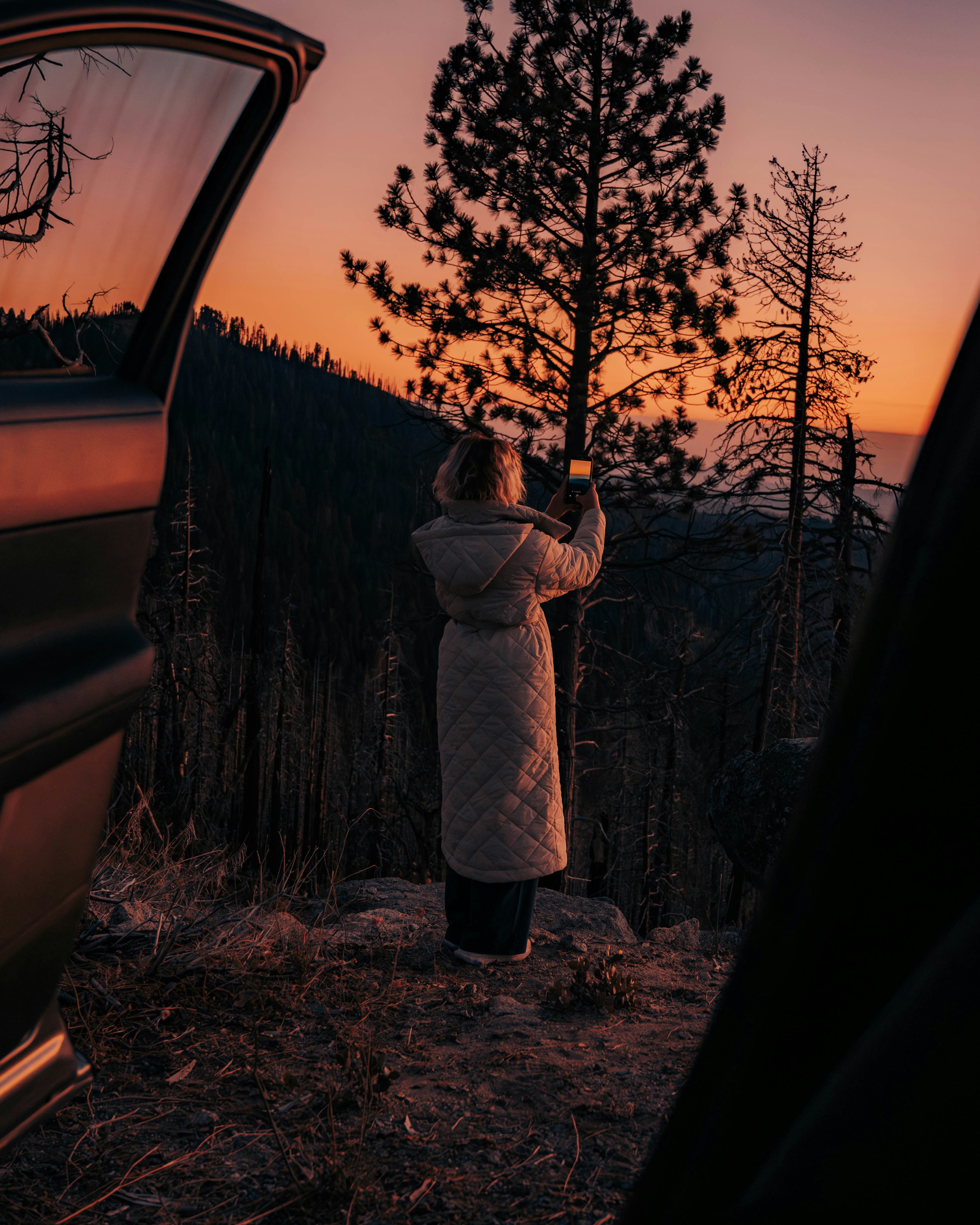 Woman photographing sunset from a car window.