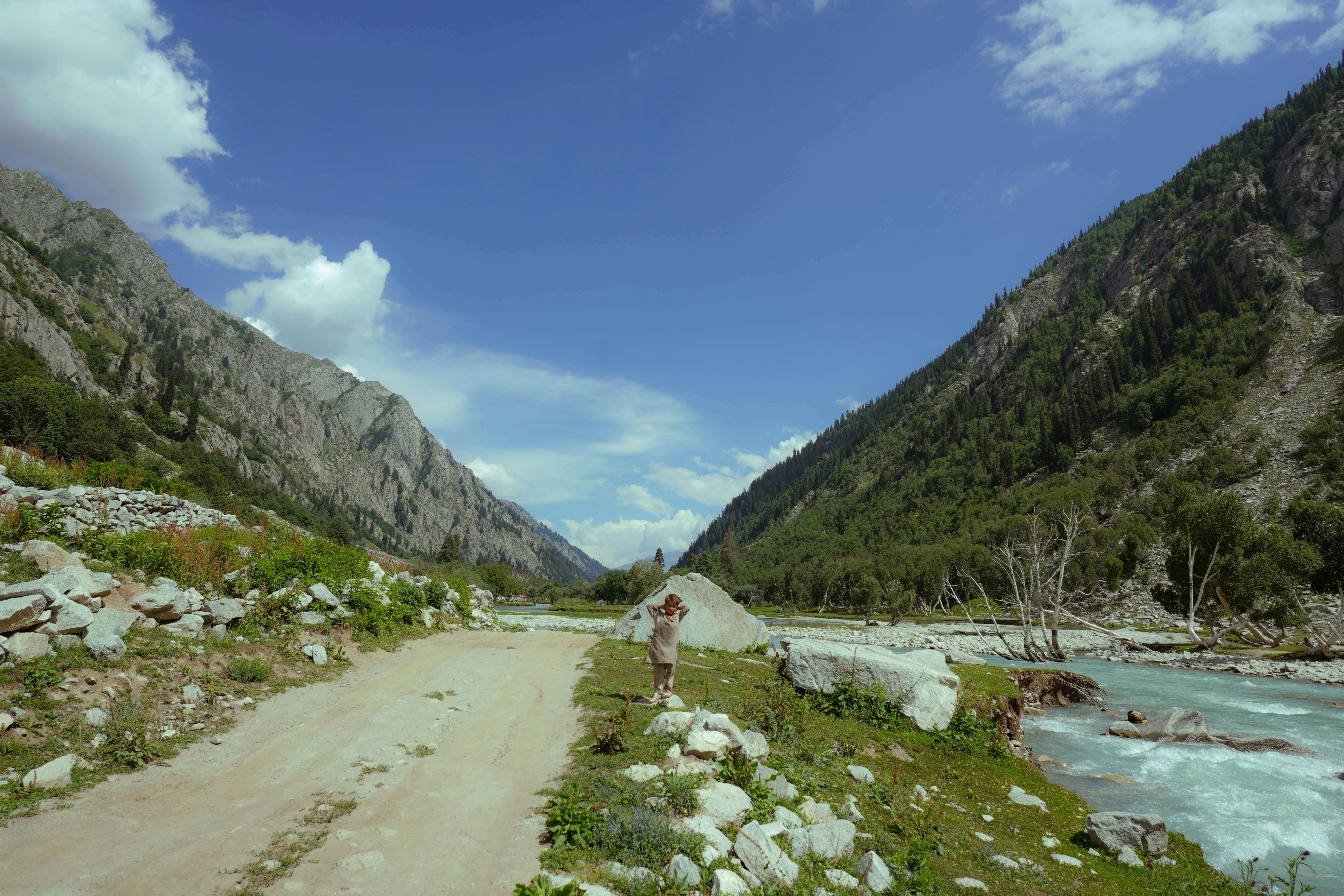 Standing on the edge of a fast-flowing river in a grand mountain pass, this image evokes a sense of adventure and awe.