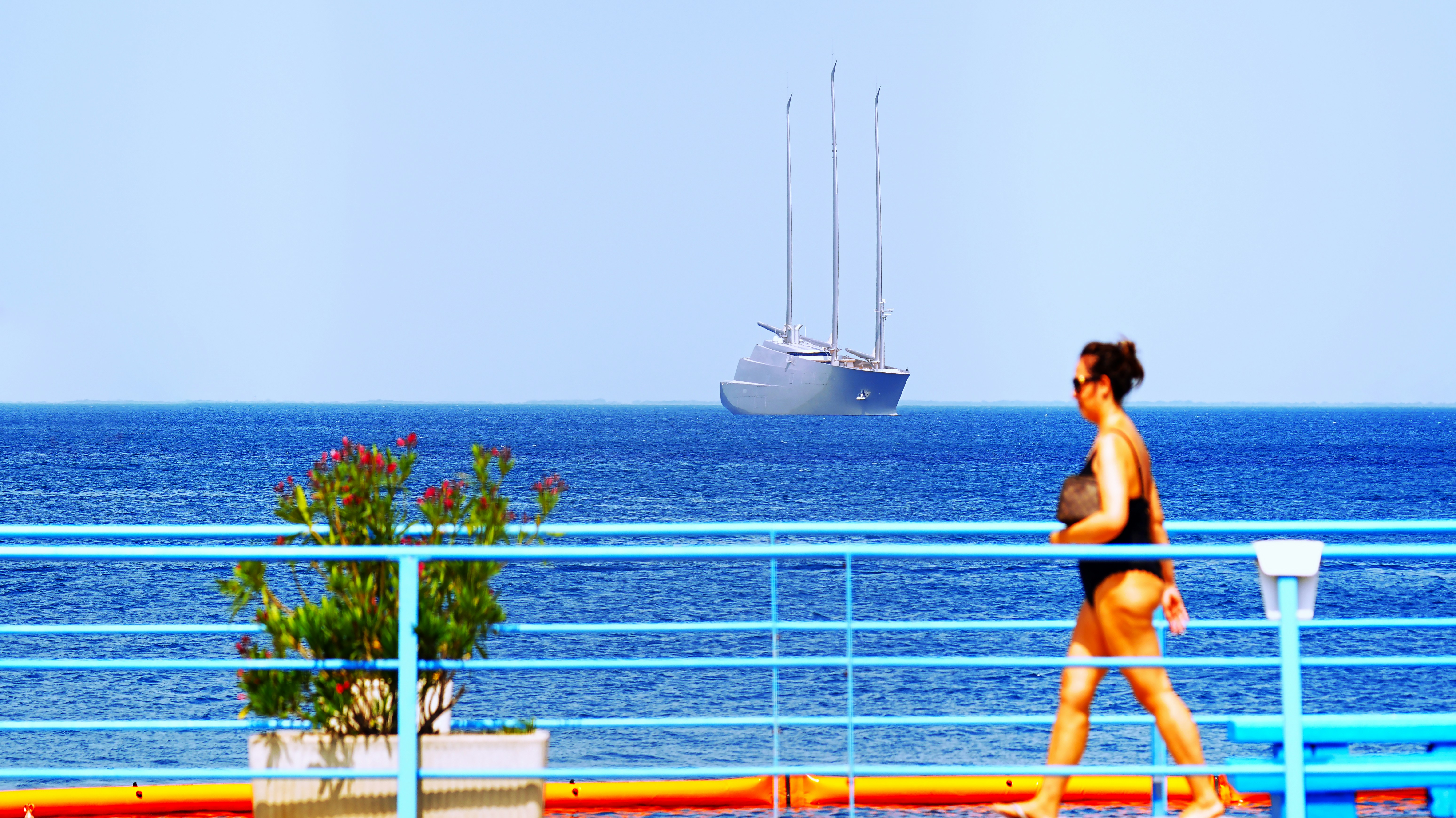 Sunlit stride along the seawall: a beachside moment framed by a distant sailboat