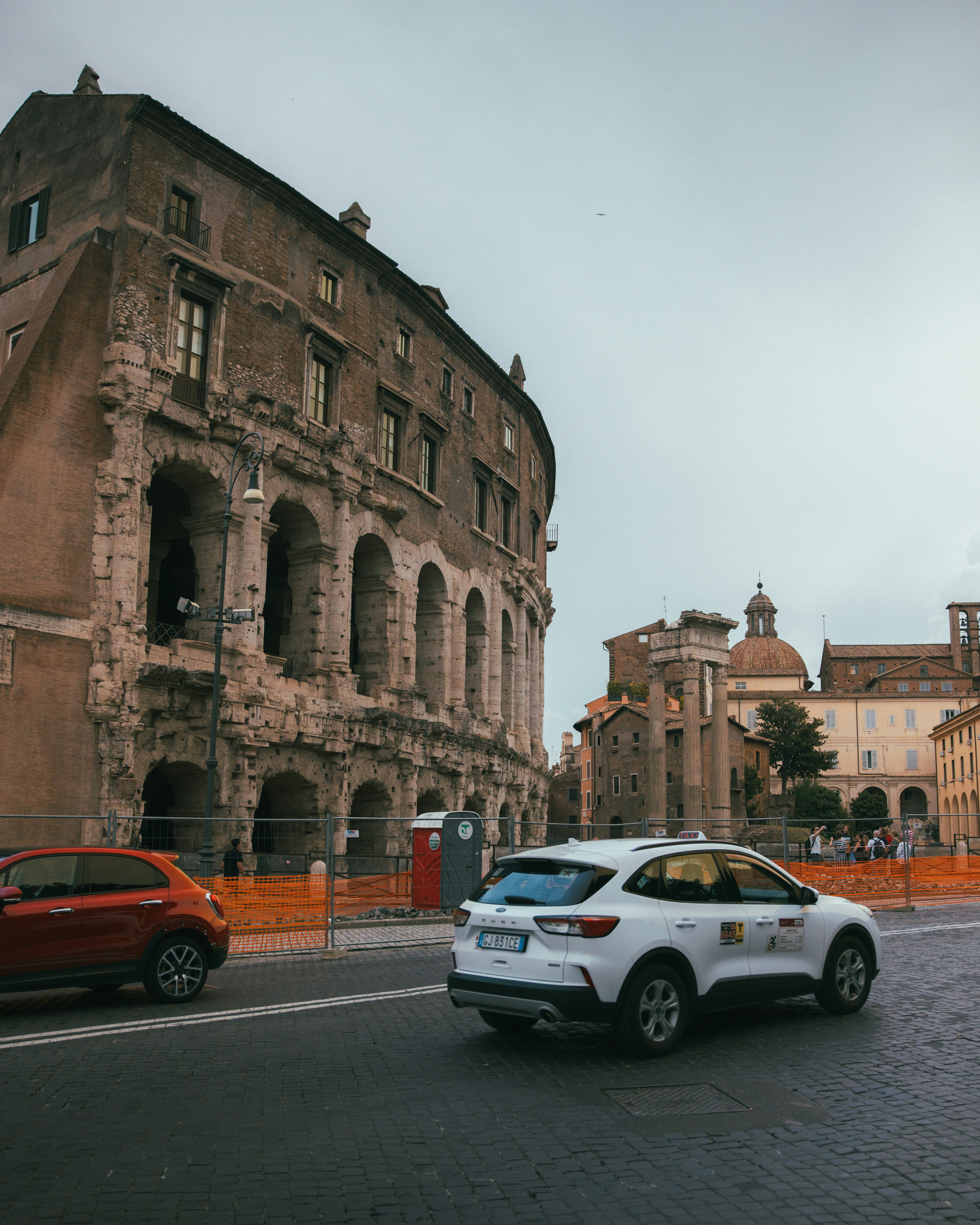 Cobbled Crossroads: A White SUV Navigates Between Ancient Arches