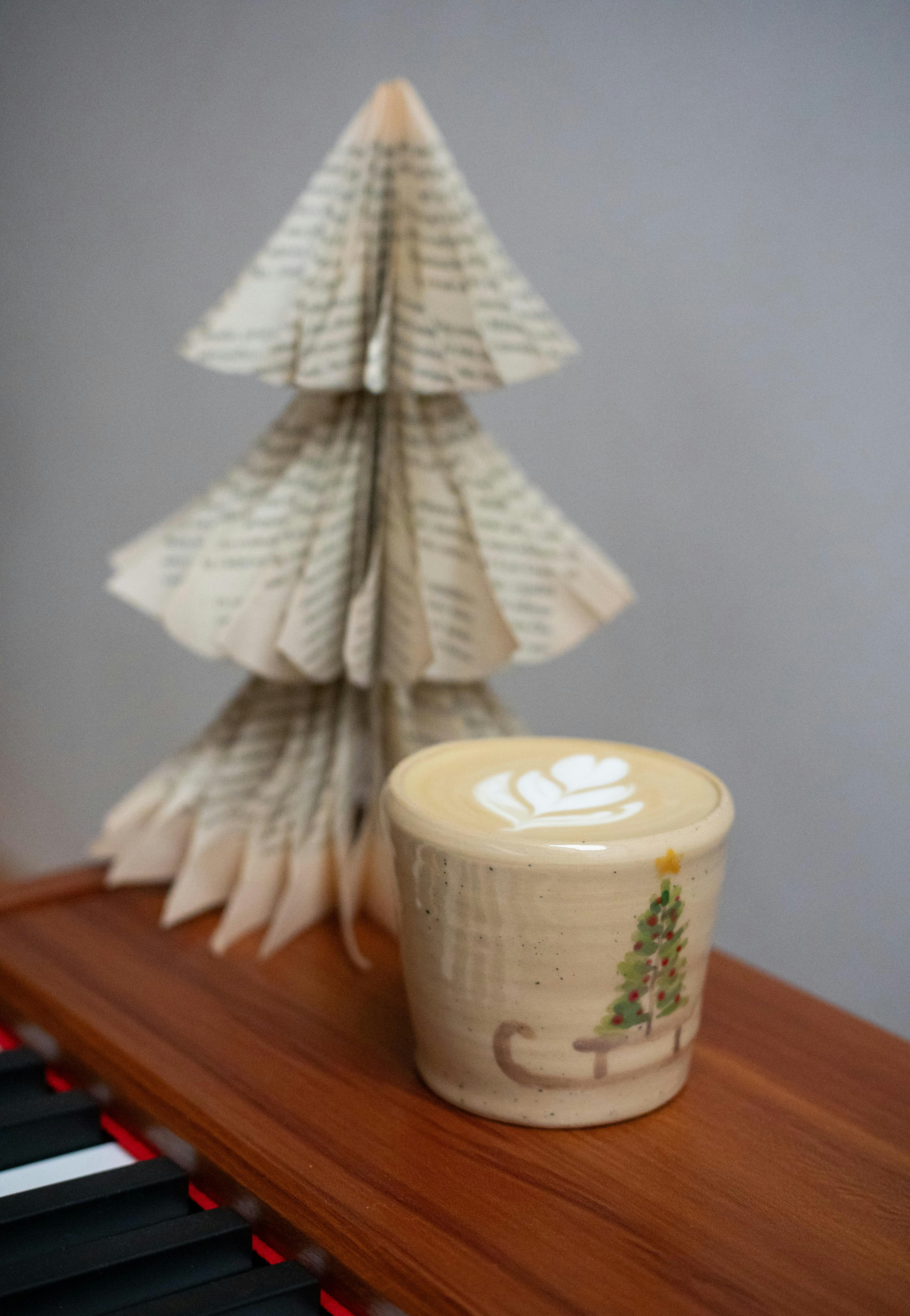 Latte art in a christmas-themed mug next to paper tree