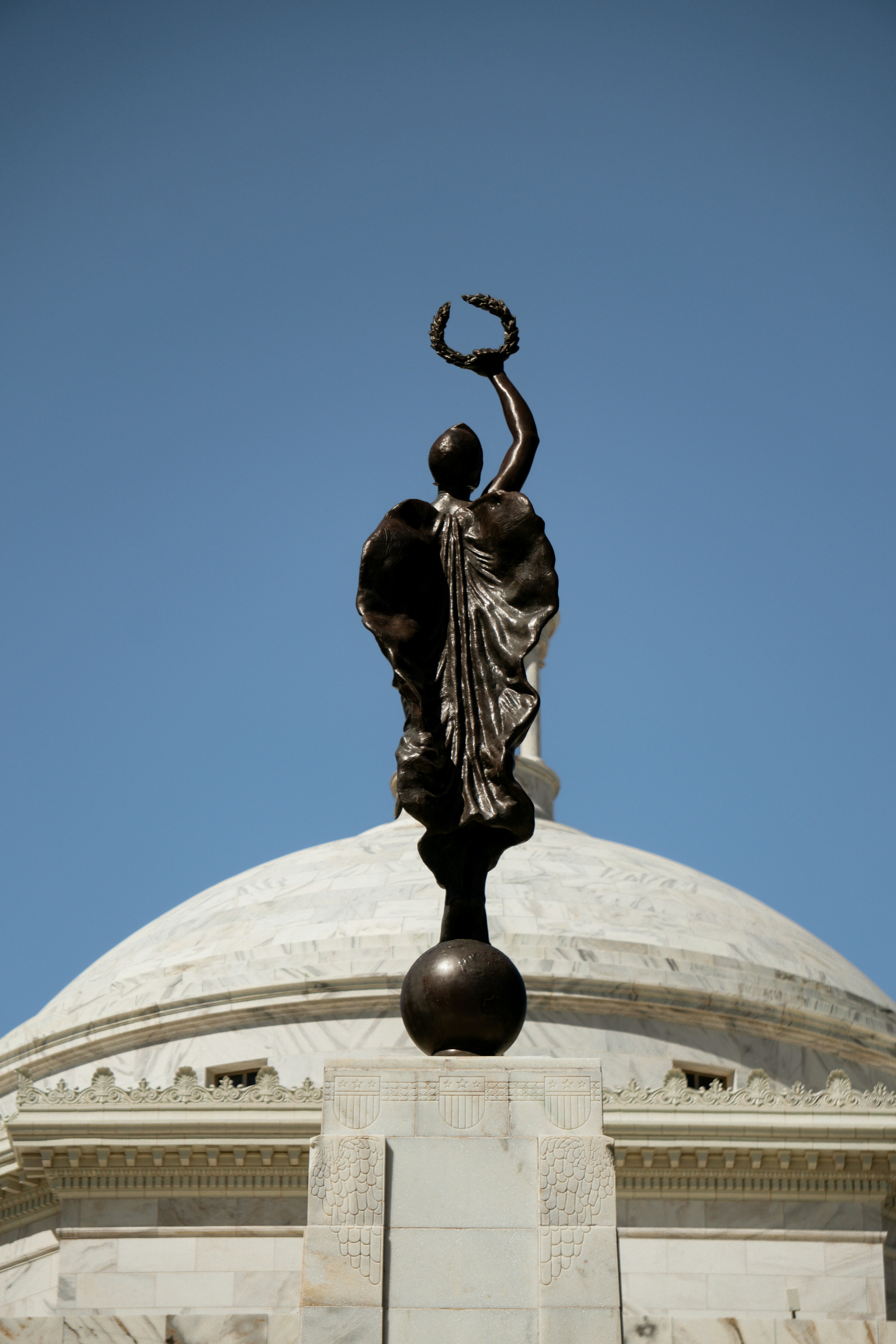 Bronze Gesture Above Marble Dome Beneath a Clear Azure Sky