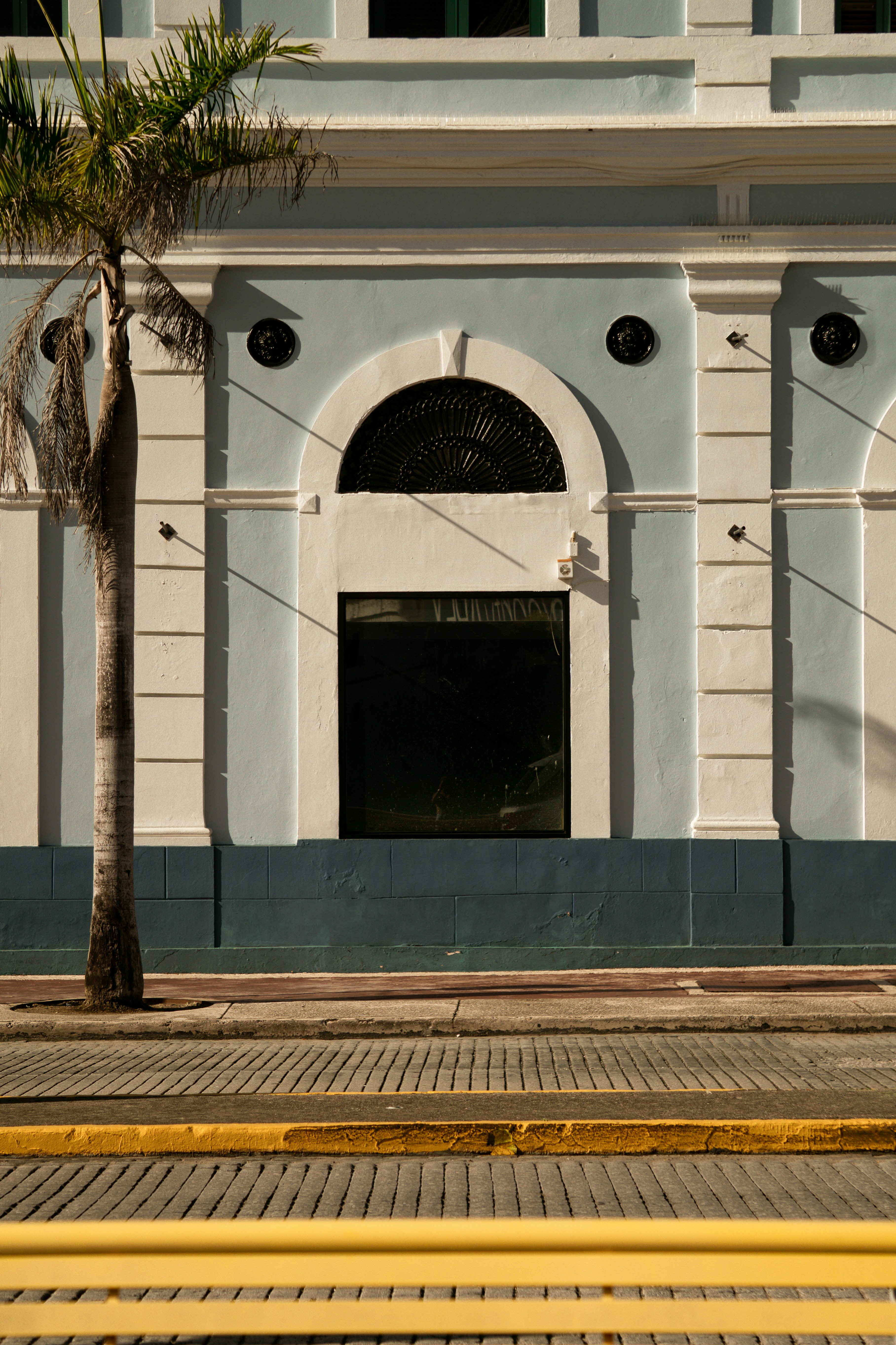 Pastel Archway on a Sunlit Street: Palm Framing the Central Façade
