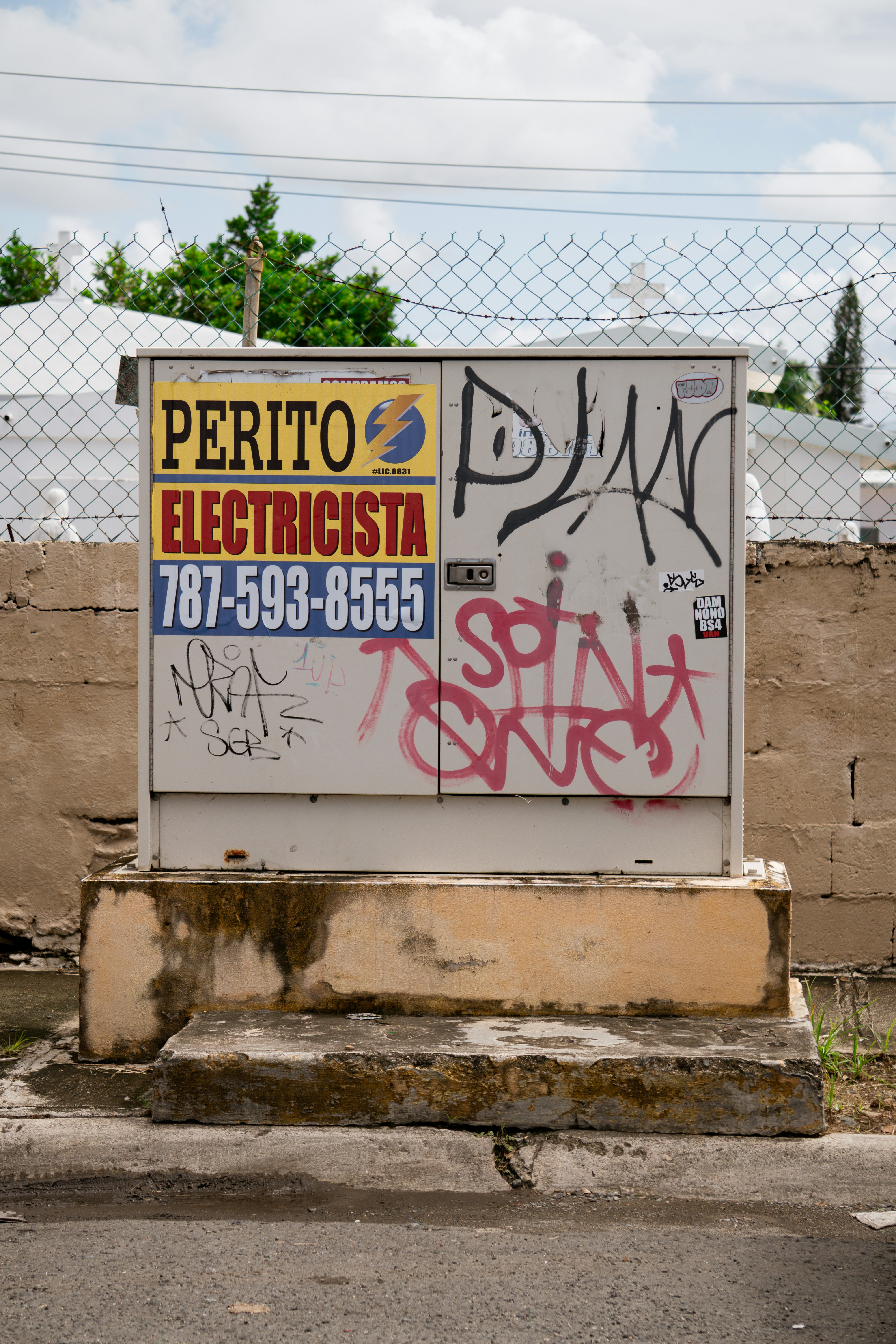 Perito Electricista Graffiti on a Weathered Utility Box by a Chain-Link Backdrop