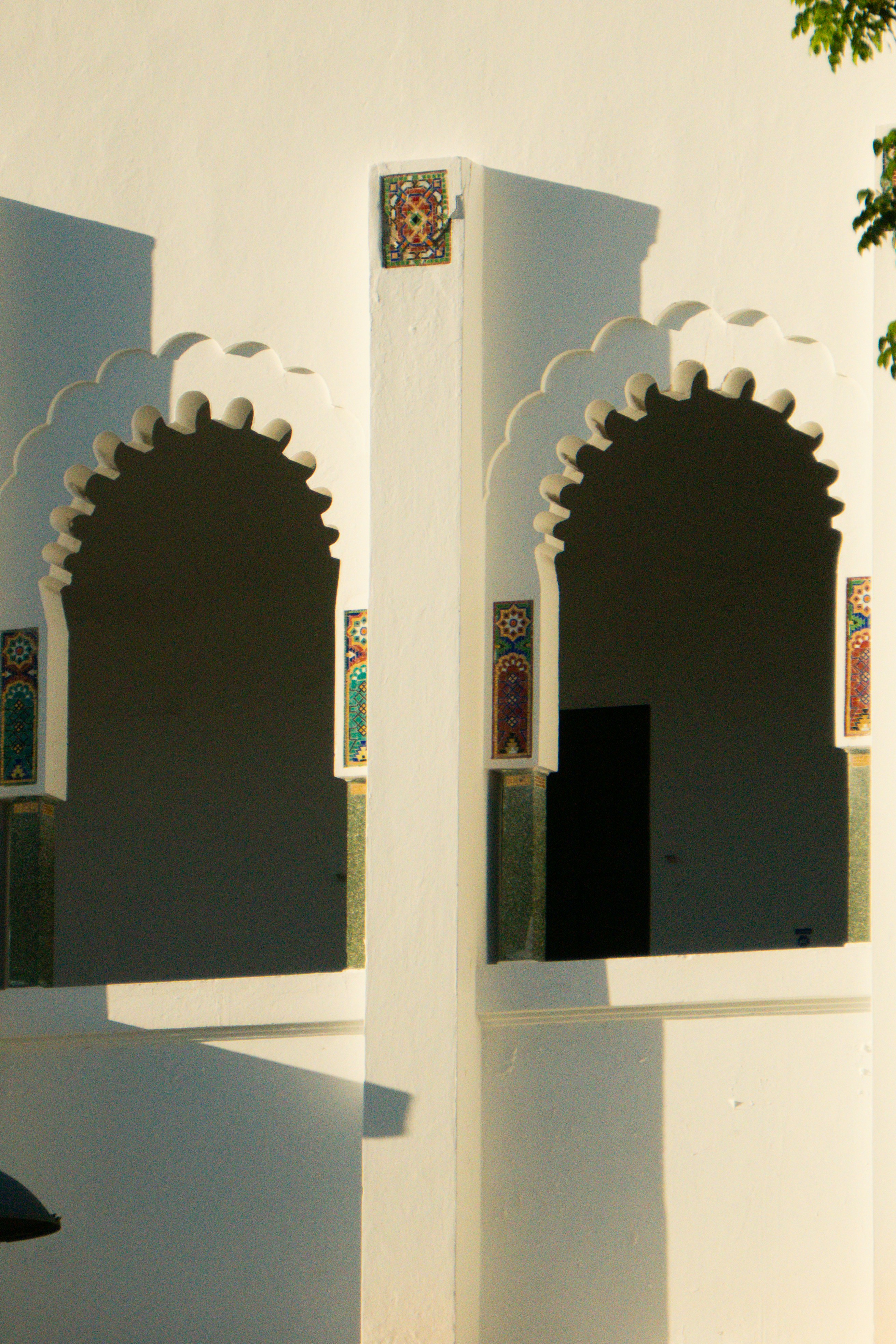 Twin Arches in Sunlit White Courtyard: Mosaic Pillar Framed by Shadow