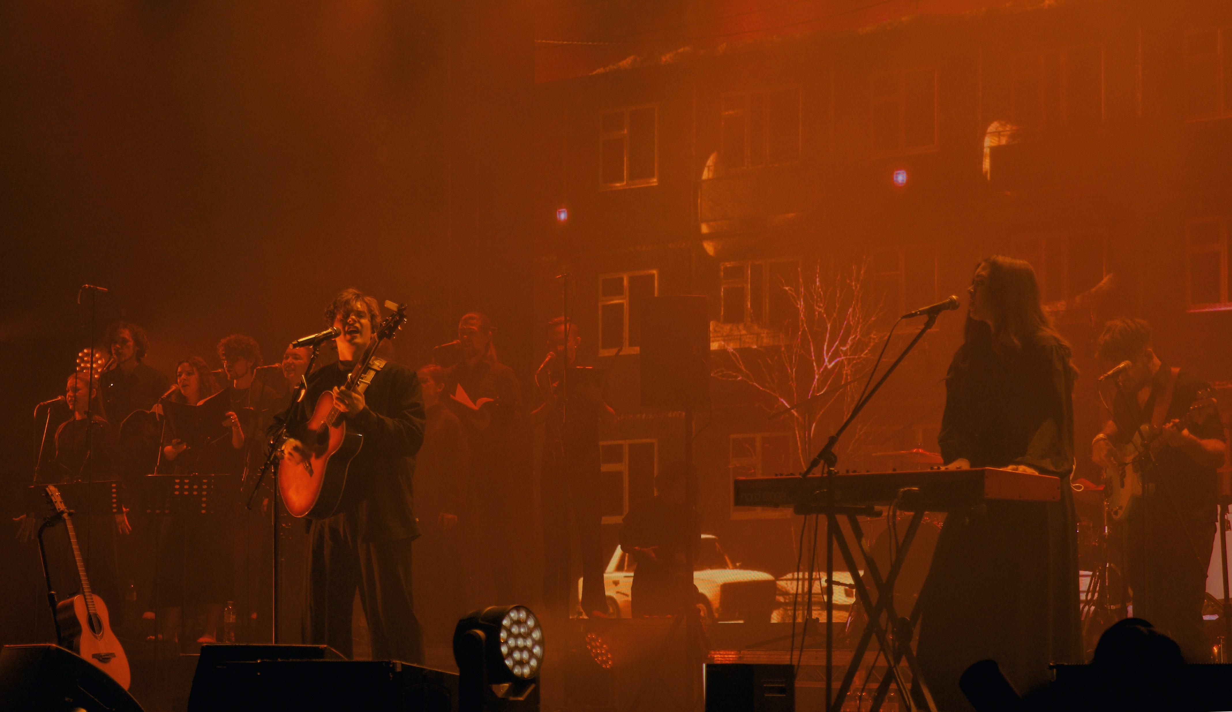 Crimson Hour on Stage: Guitarist Centered in a Warm Orange Glow with a Keyboardist in the Wings