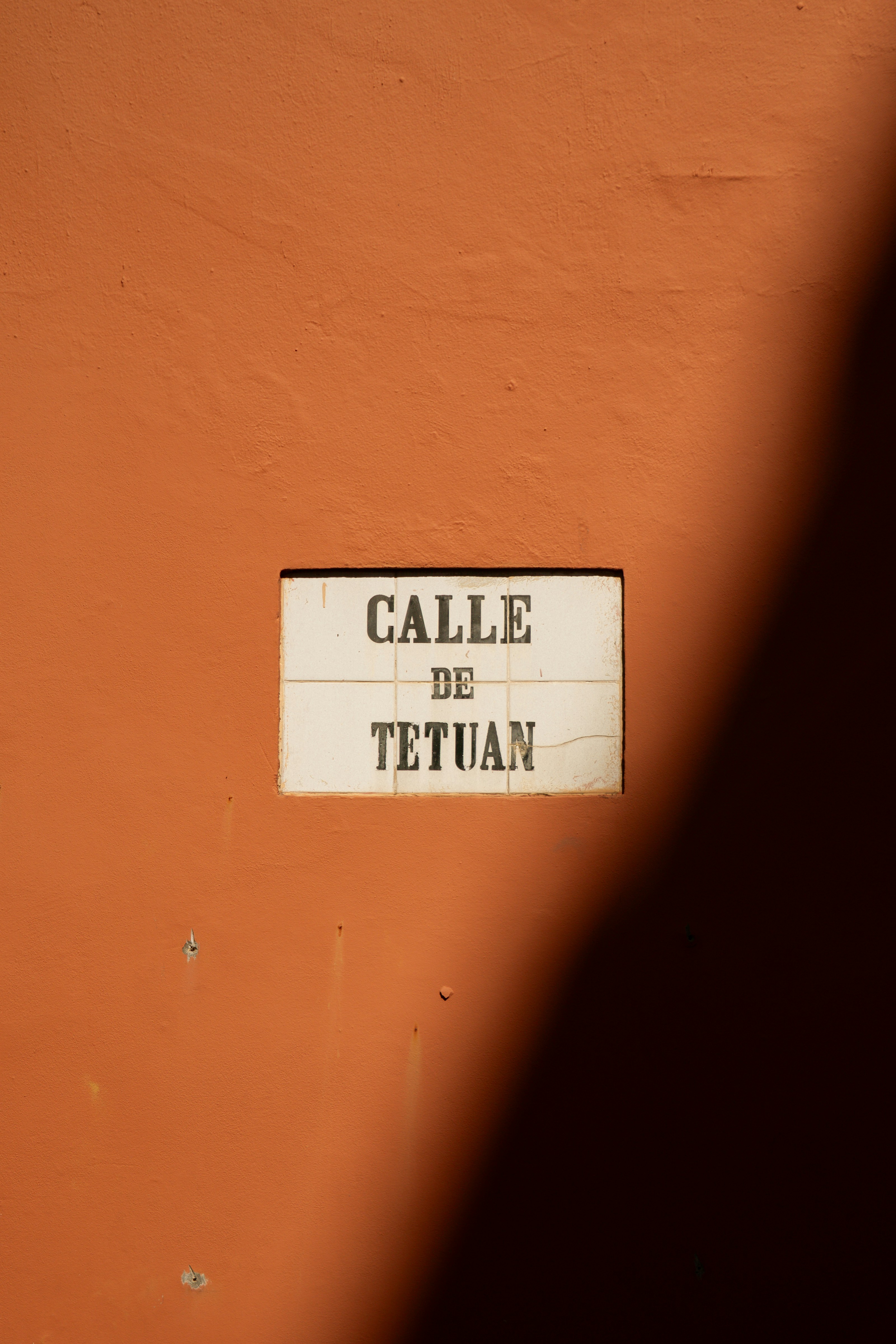 Calle de Tetuan: a sun-warmed street sign punctuating a terracotta wall with a dramatic diagonal shadow