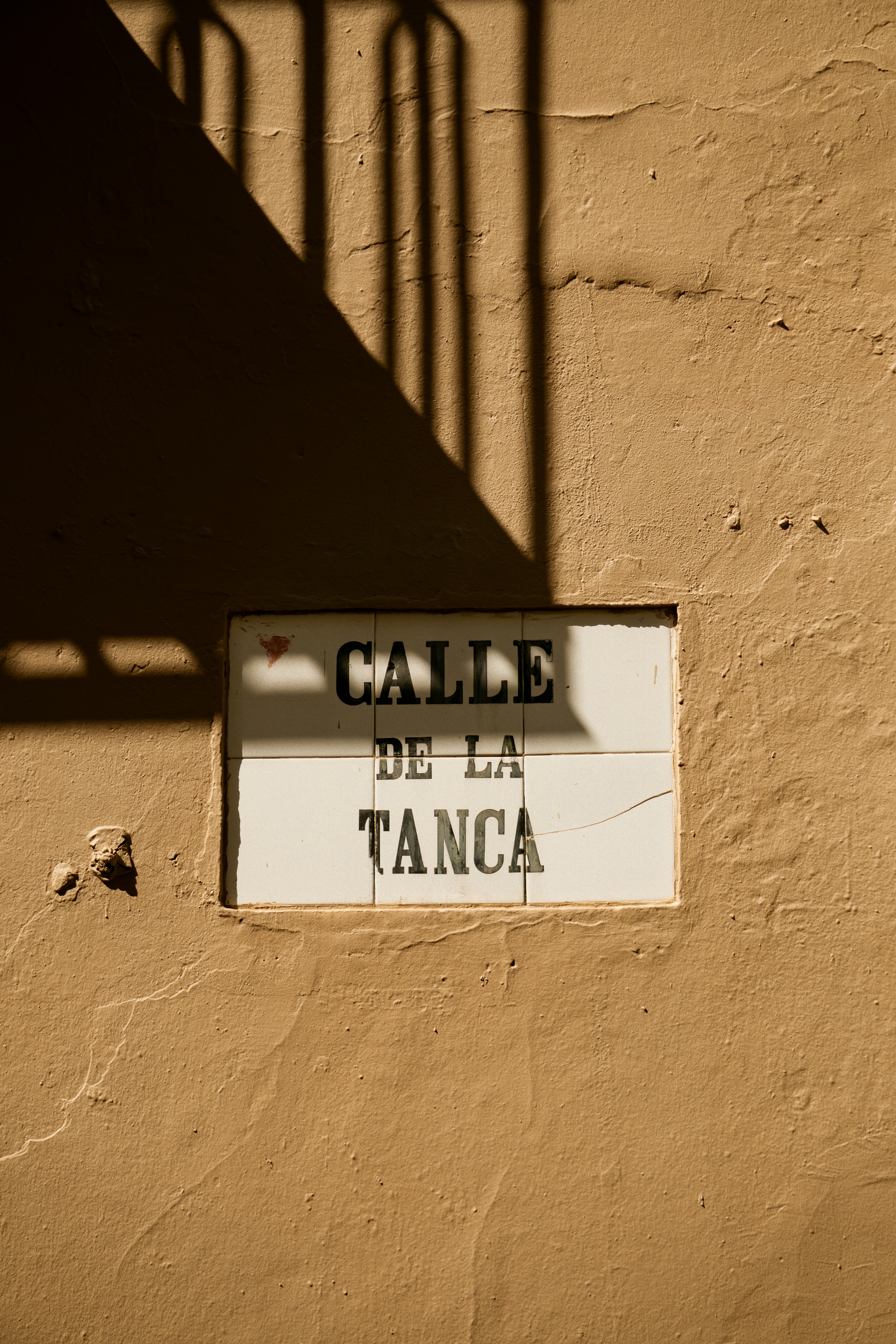 Calle de la Tanca: Sun-Warmed Wall with a Shadowed Street Sign