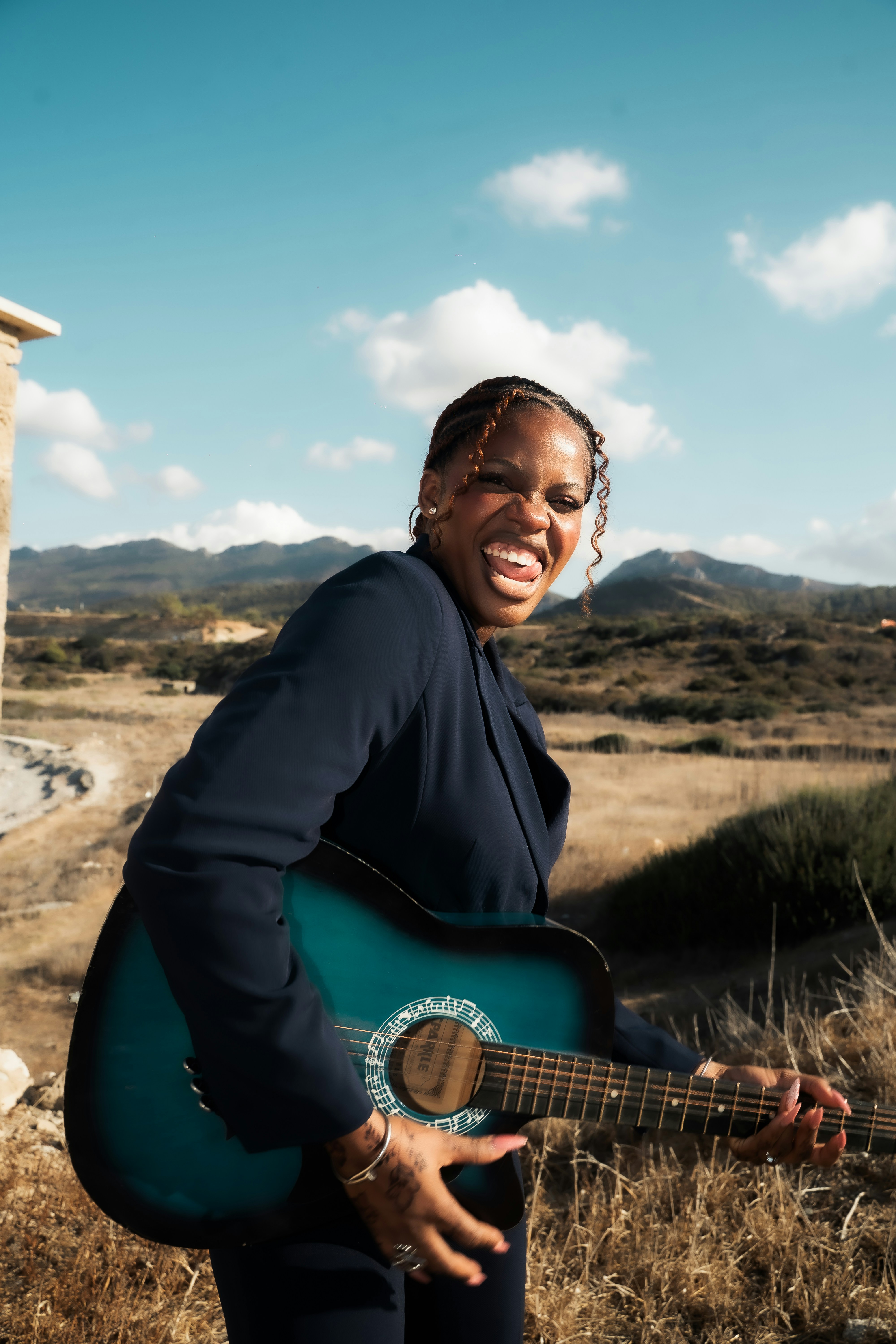 A vibrant, empowering portrait of a woman in a navy blue suit posing with attitude near the beach. The photo captures confidence, freedom, and individuality against a bright coastal backdrop — a fusion of style and energy under clear blue skie