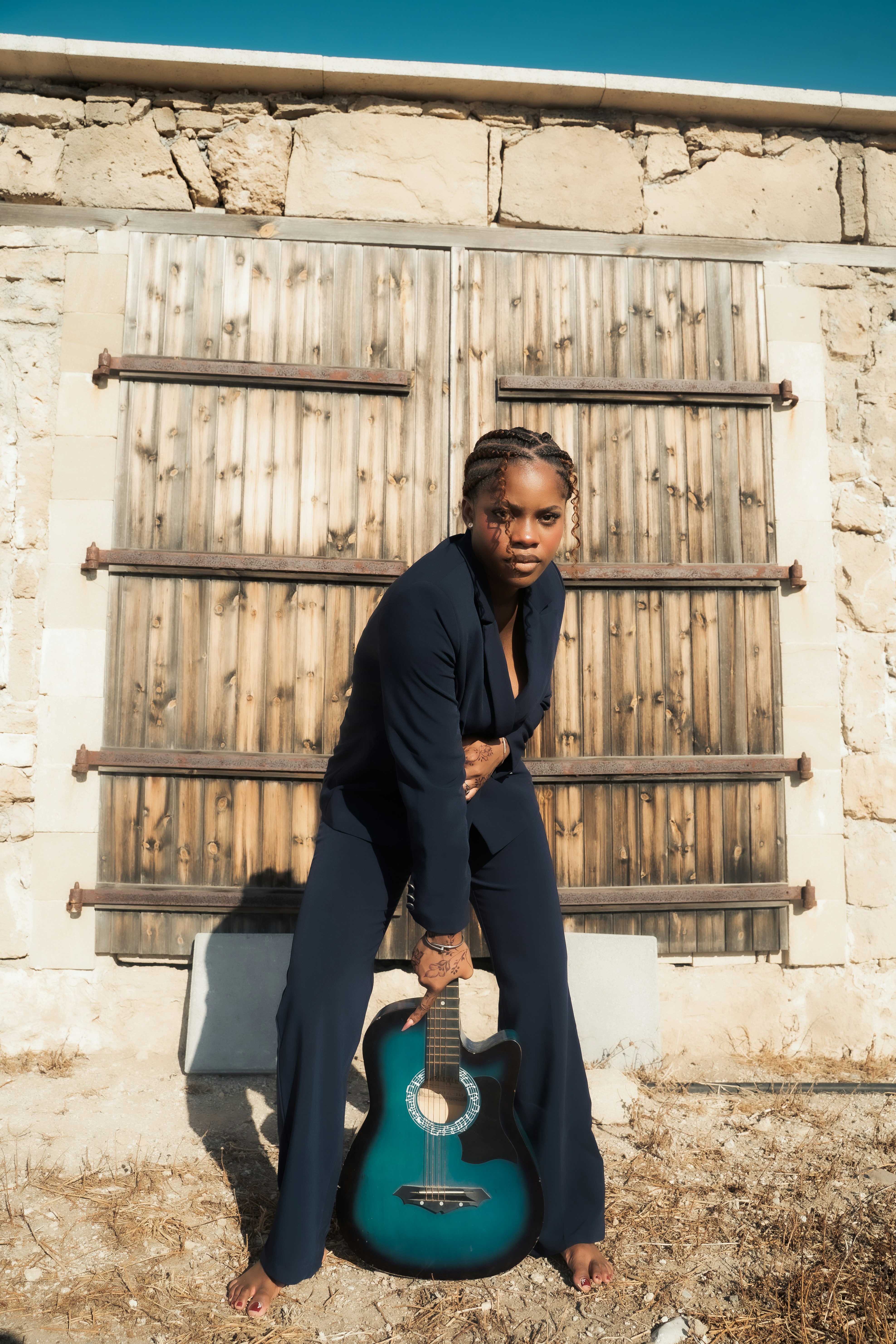 A vibrant, empowering portrait of a woman in a navy blue suit posing with attitude near the beach. The photo captures confidence, freedom, and individuality against a bright coastal backdrop — a fusion of style and energy under clear blue skie