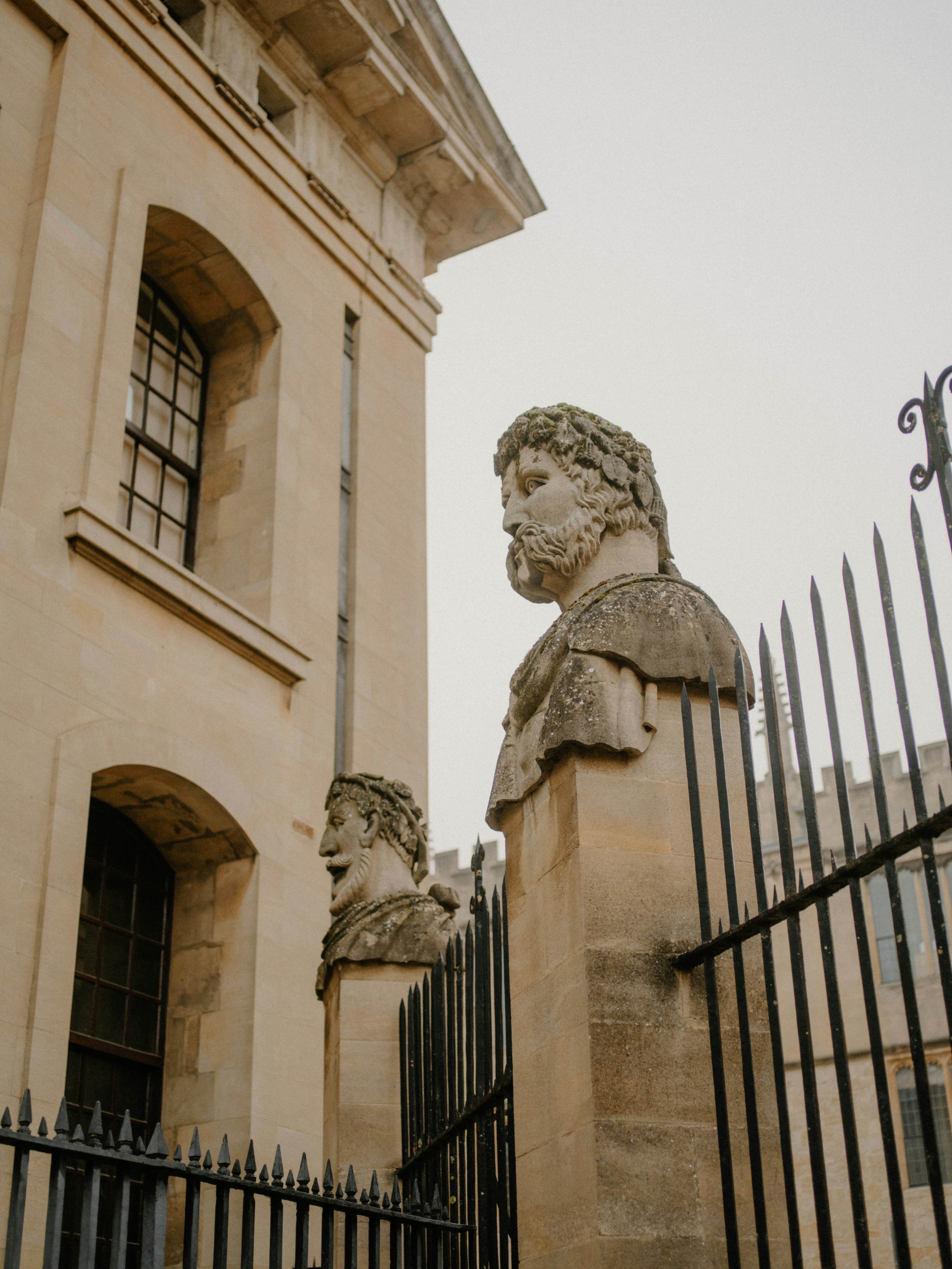 Guardians of the Gate: Weathered Busts Over a Wrought-Iron Barrier