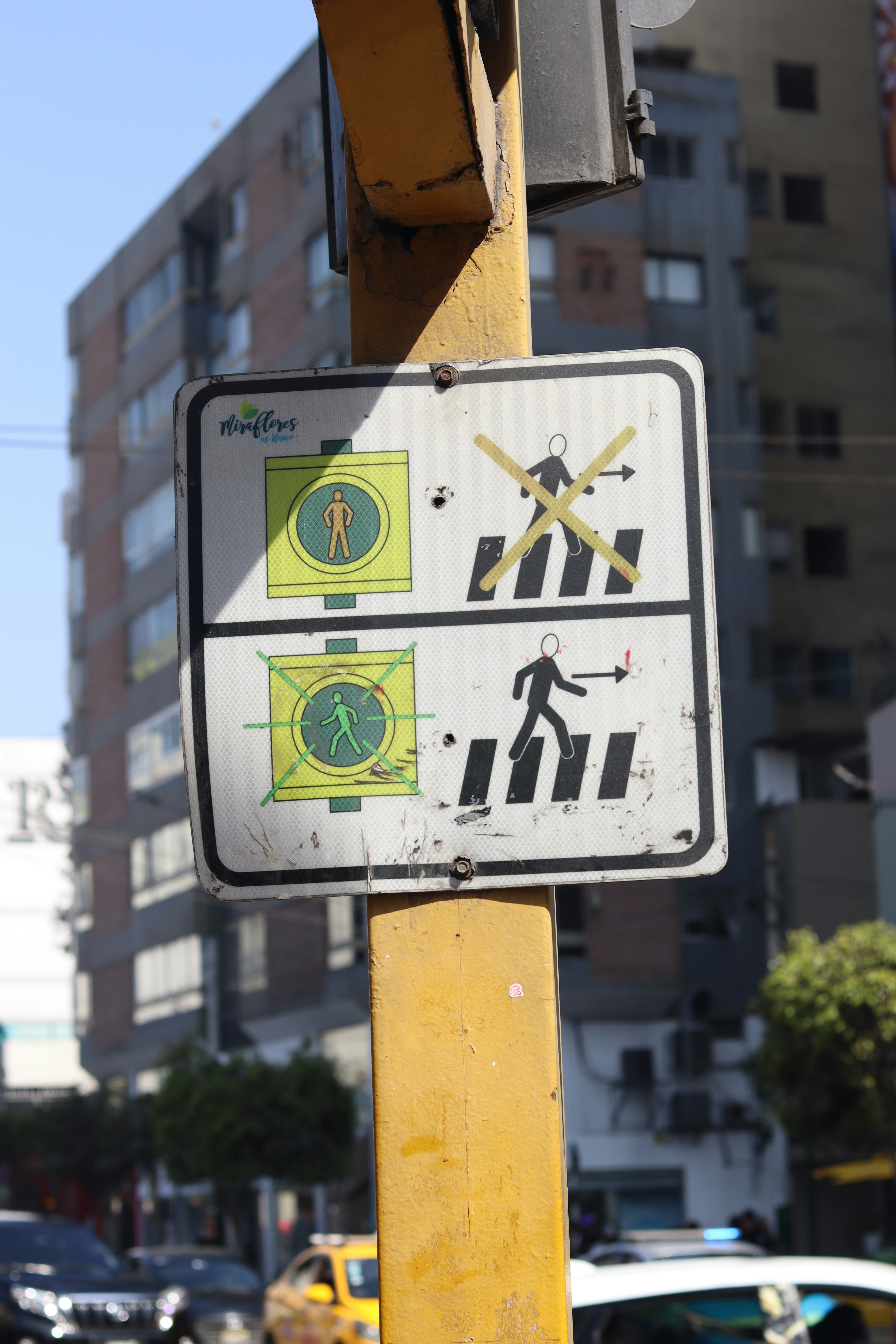 Urban Crosswalk Chronicle: A Weathered Safety Sign on a Sunlit Pole