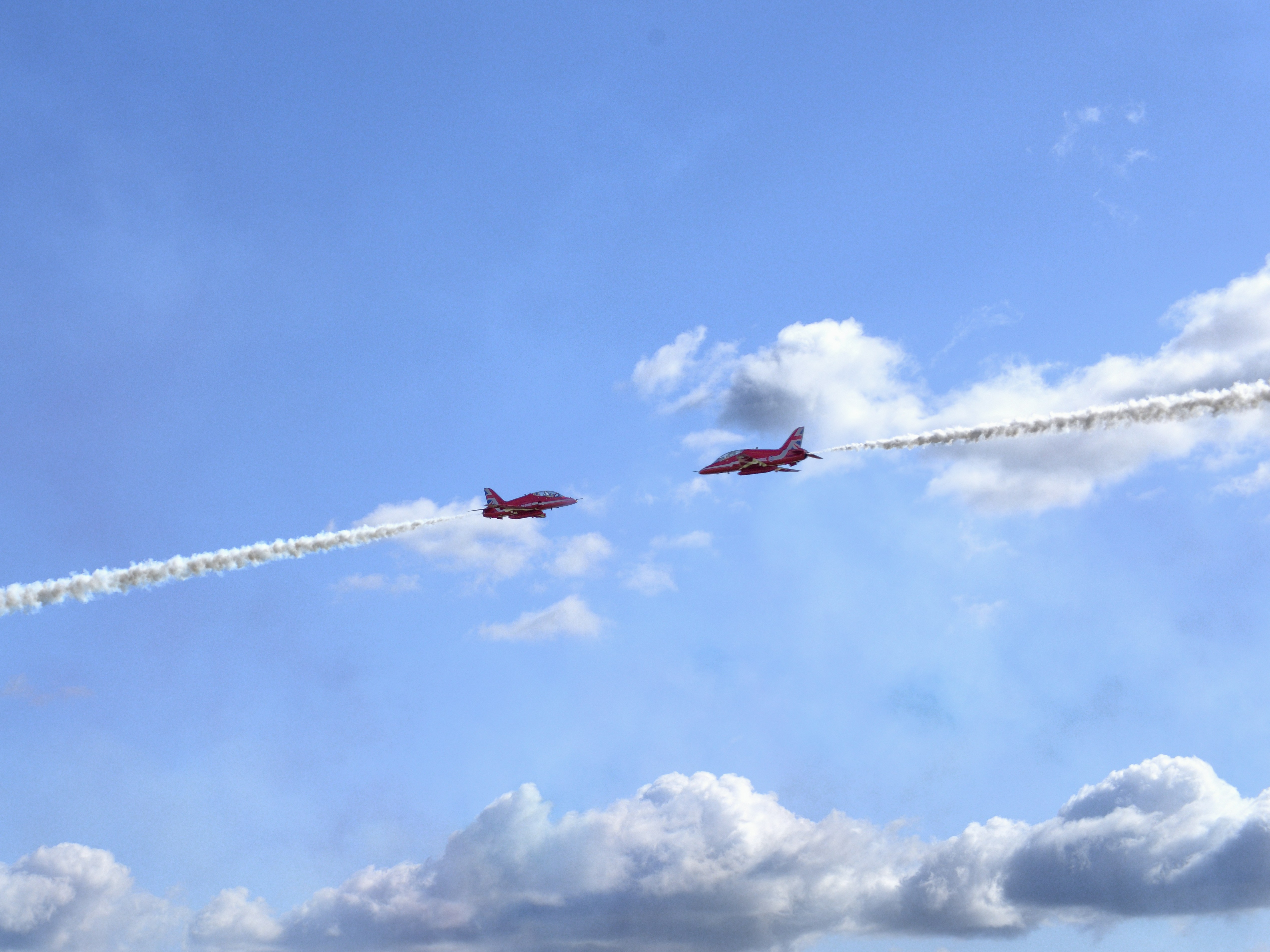 Crimson Jets Carve a Sky-Blue Ribbon Over Puffy Clouds