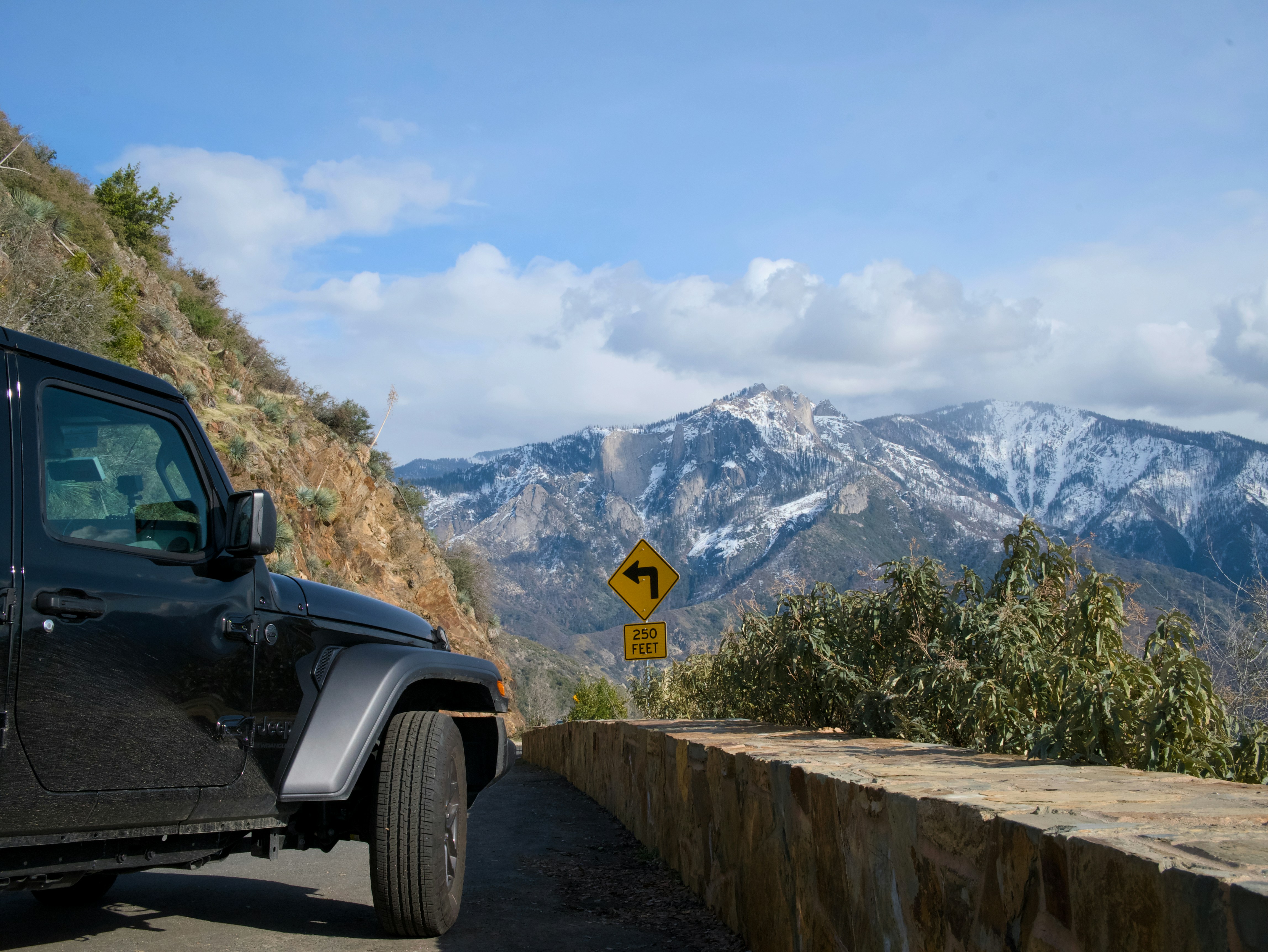 Cliffside Vista: Jeep Pauses as Snow-Dusted Peaks Rise