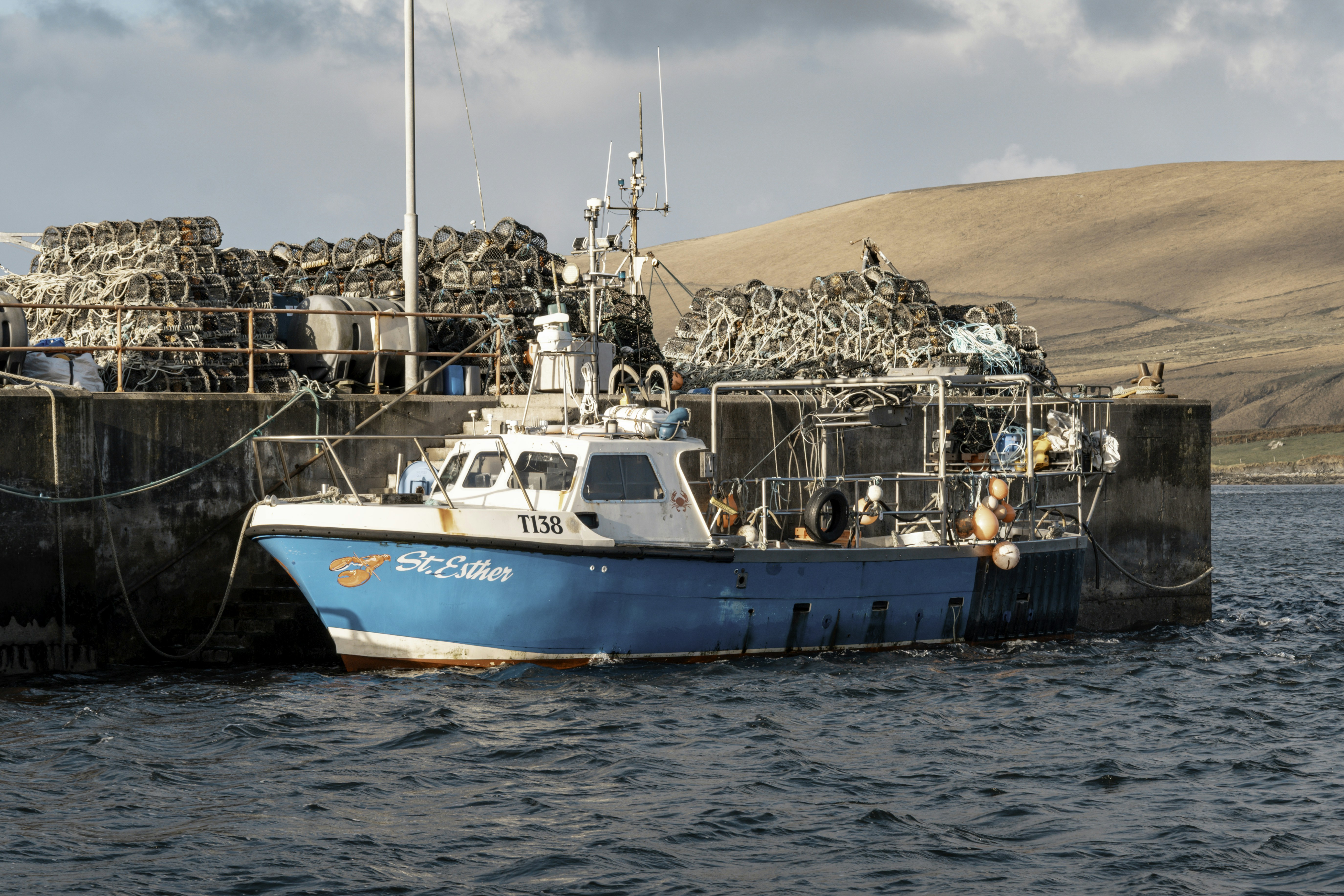 Blue fishing boat docked next to stacked crab pots. photo – Free Sea ...