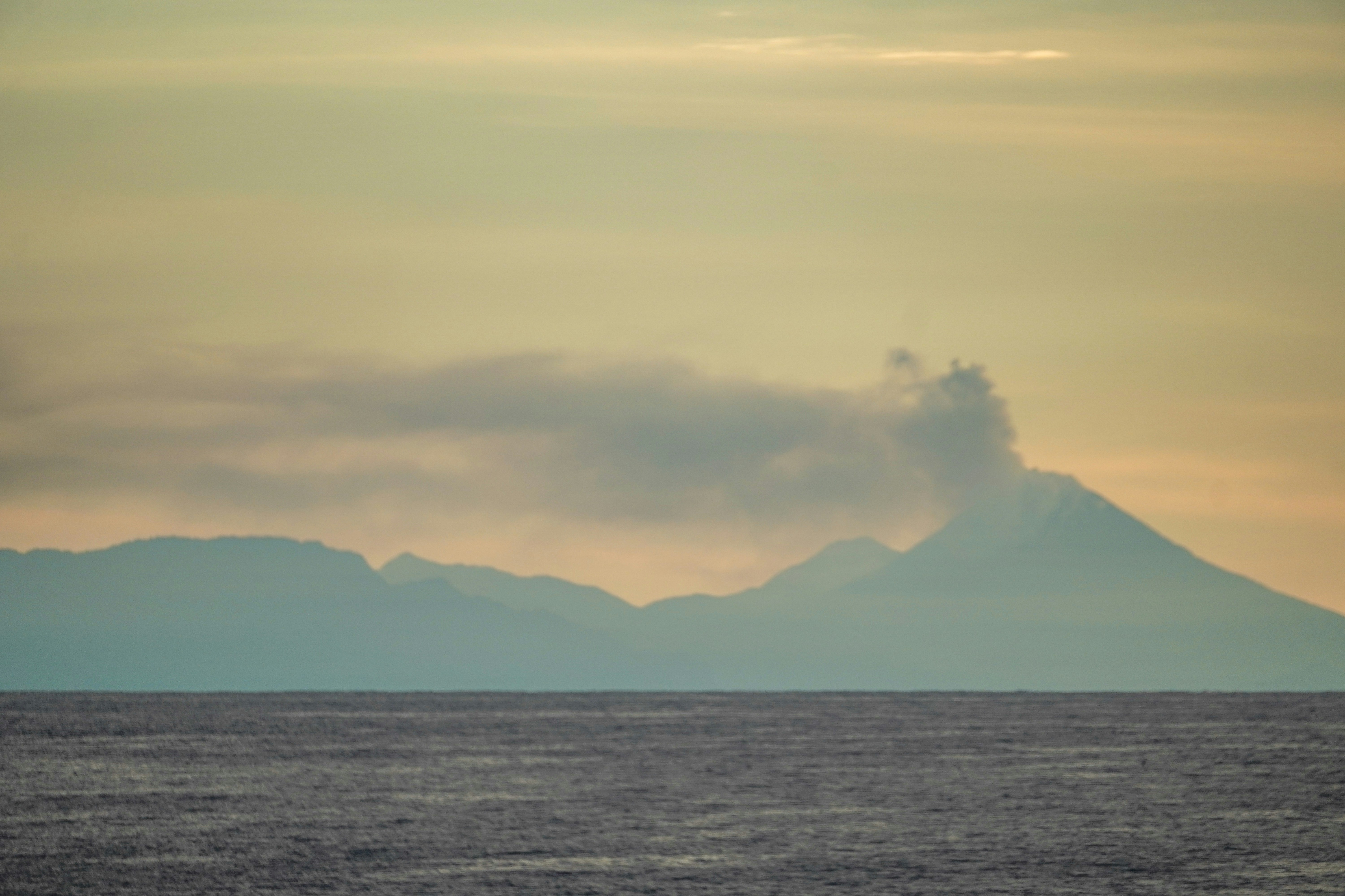 Horizon Crown: A Distant Peak Looms Over a Calm Sea at Sunset