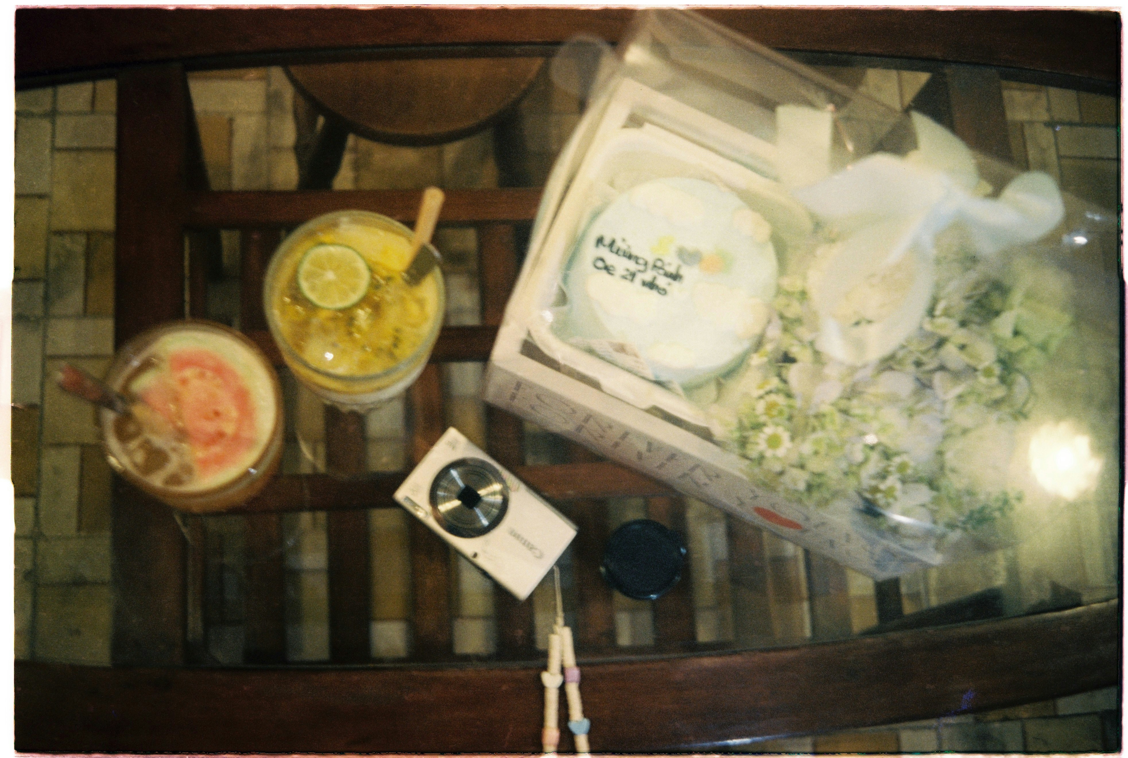 Overhead Feast: Cake Box, Drinks, and a Tiny Camera on a Wooden Table