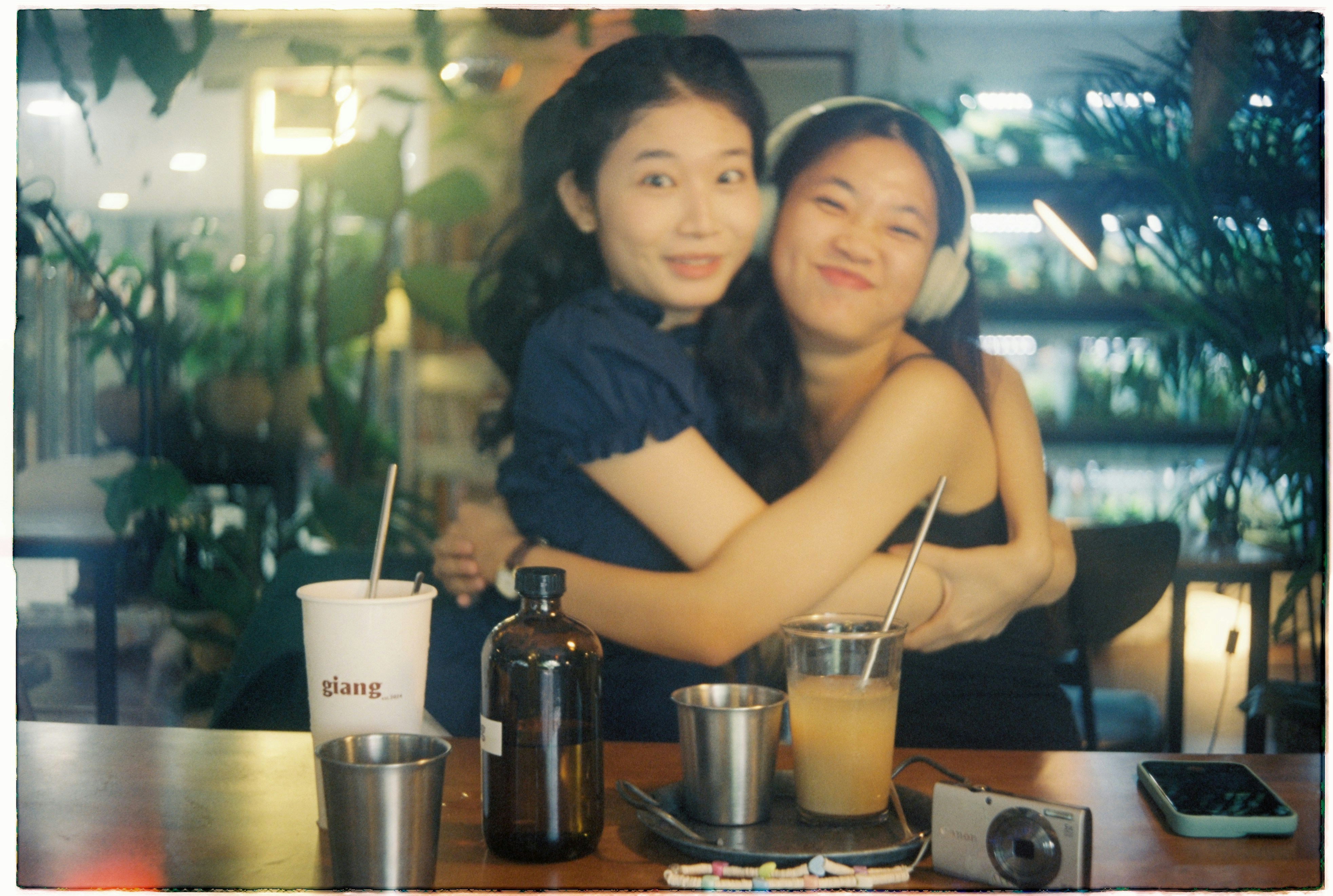 Cafe Embrace: Two Friends, Warm Light, and a Small Camera on the Table