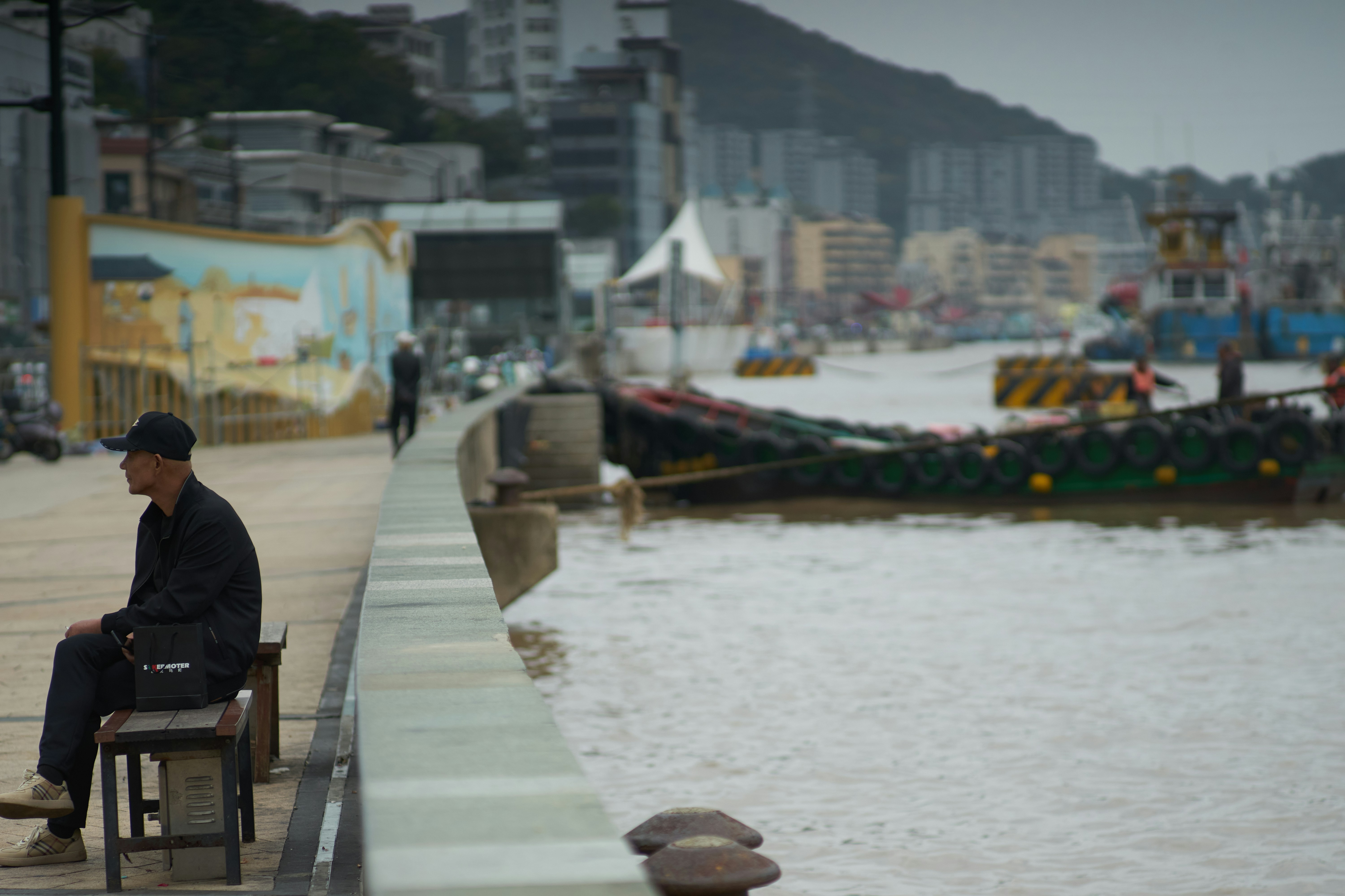Quayside Quiet: A Solitary Figure Anchored by the Harbor