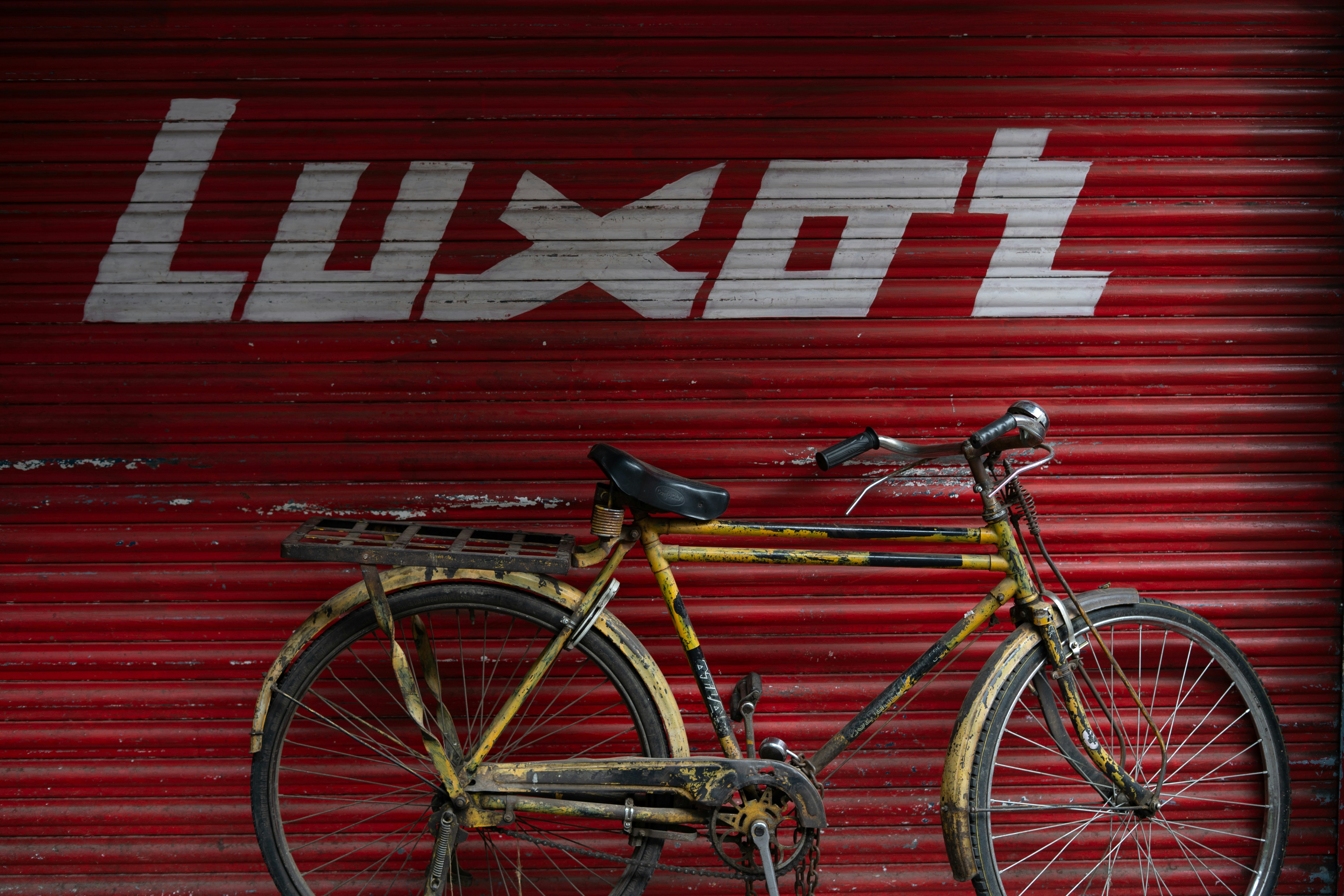 Scarlet Shutter, Worn Wheels: A Yellow Bicycle Stubbornly Resting Against a Red Facade