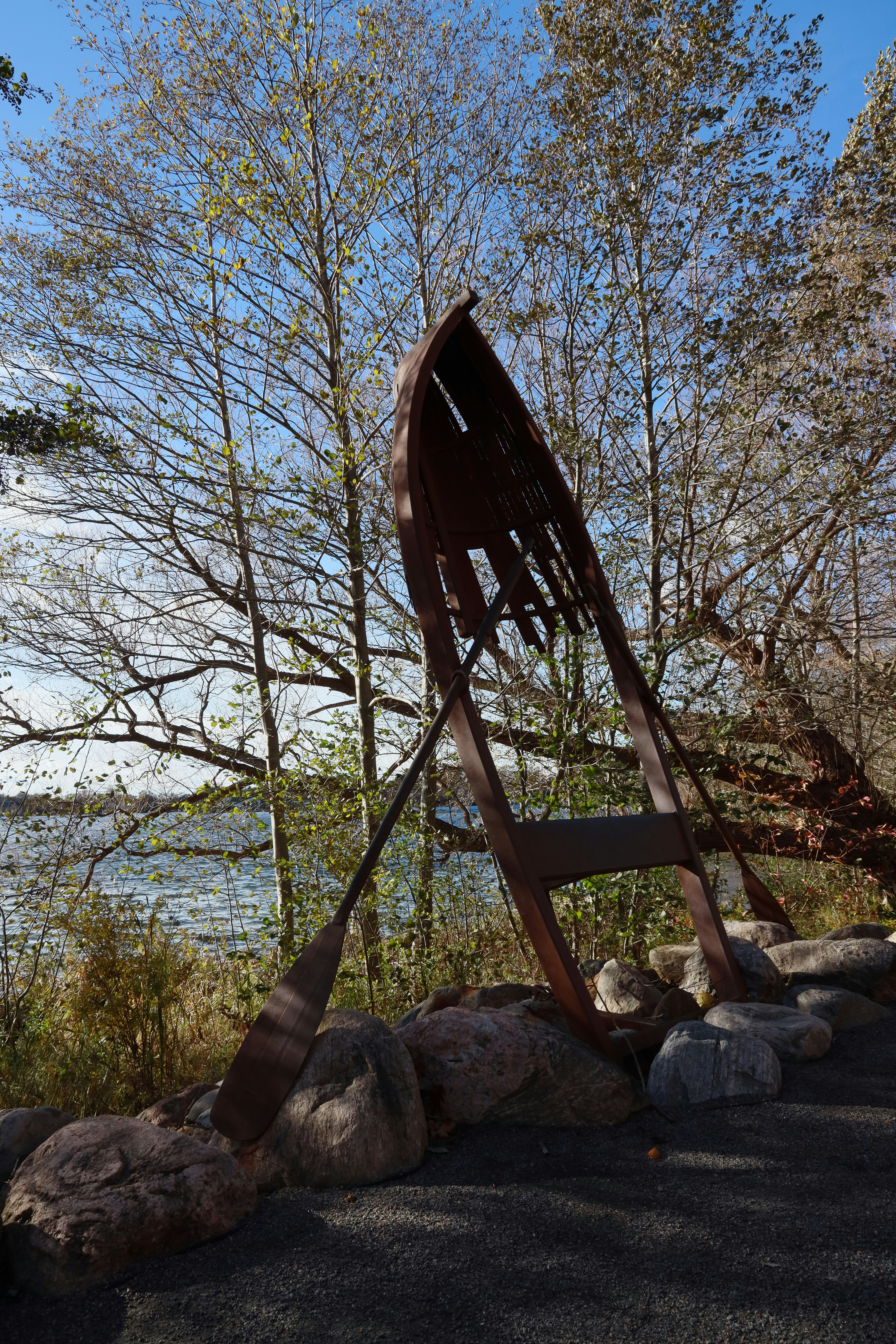 Rust Arc by the Lake: A Leaning Chair Sculpture Framed by Trees