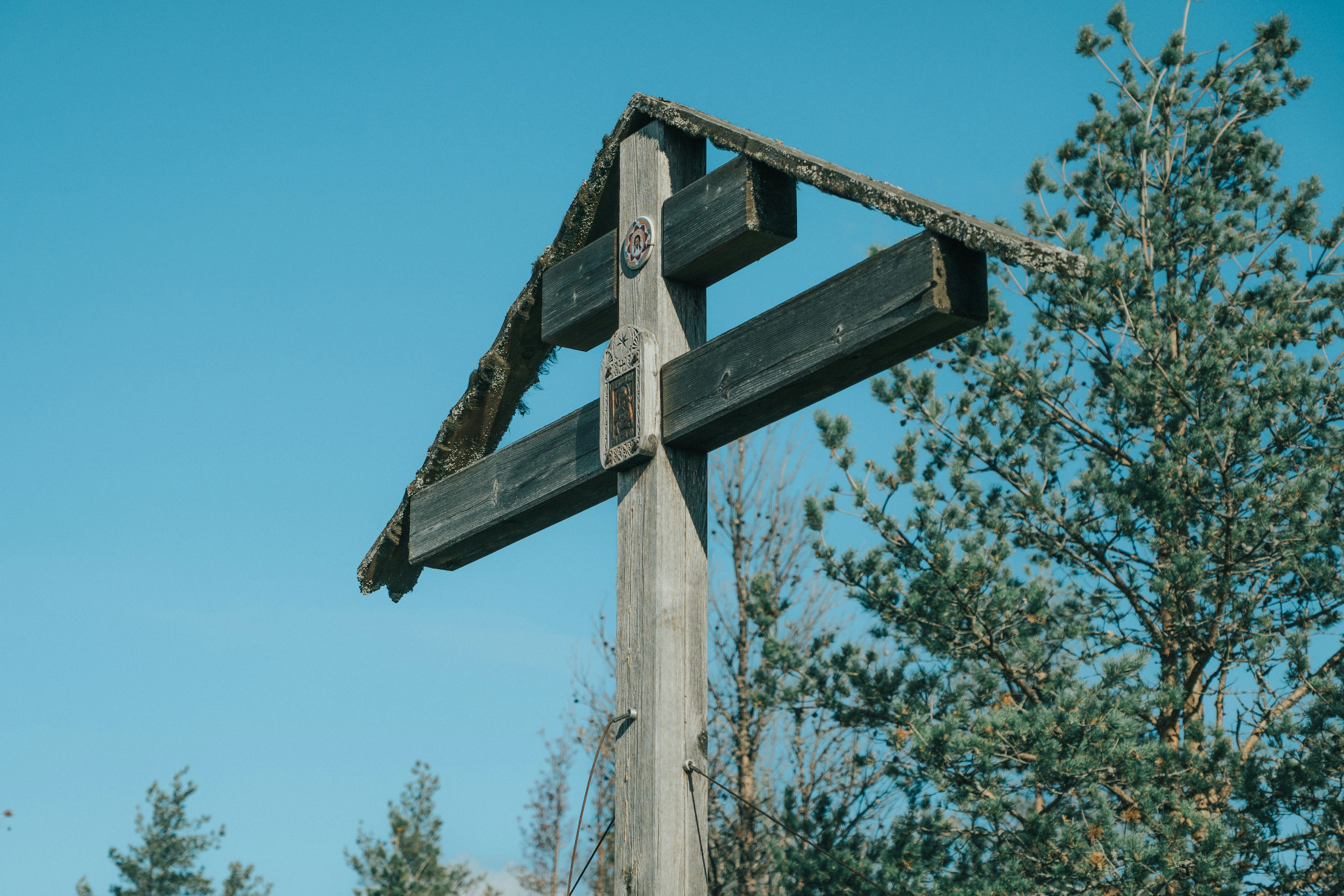 Wooden Orthodox cross on the top of Mount Riuttavuori, Riekkalansaari Island, Lake Ladoga. The cross, sheltered by a small roof and adorned with an icon, stands as a spiritual landmark of remembrance. Surrounded by pines and set against the clear northern sky, it captures the peaceful solitude of Karelia’s nature.