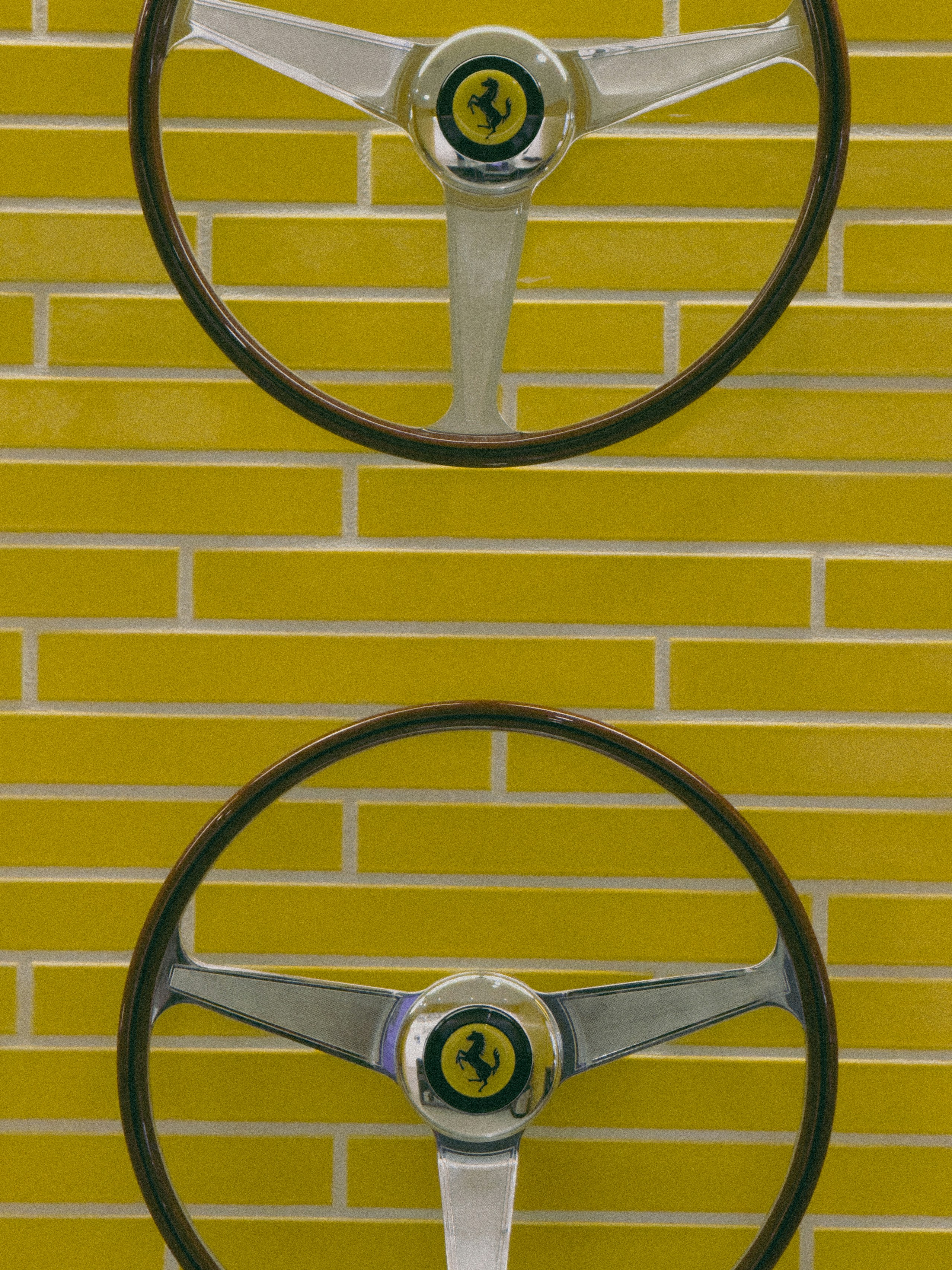 Chrome Halos: twin Ferrari steering wheels framed by a yellow brick wall