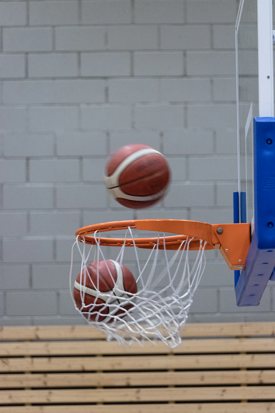 Basketball slicing through an orange rim and white net against a brick gym wall backdrop.