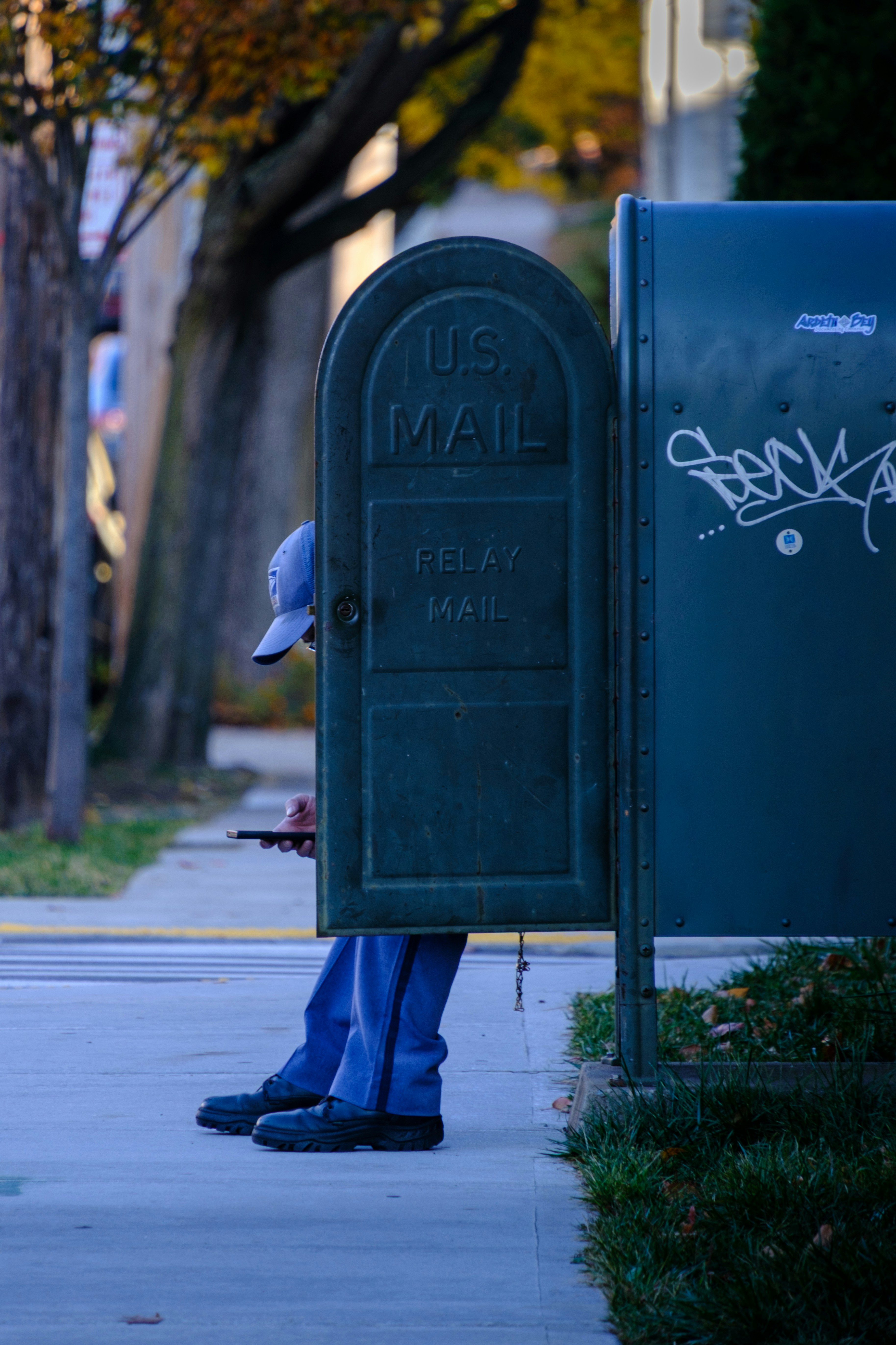Behind the Mailbox: A Quiet Phone Moment on a Leafy Street