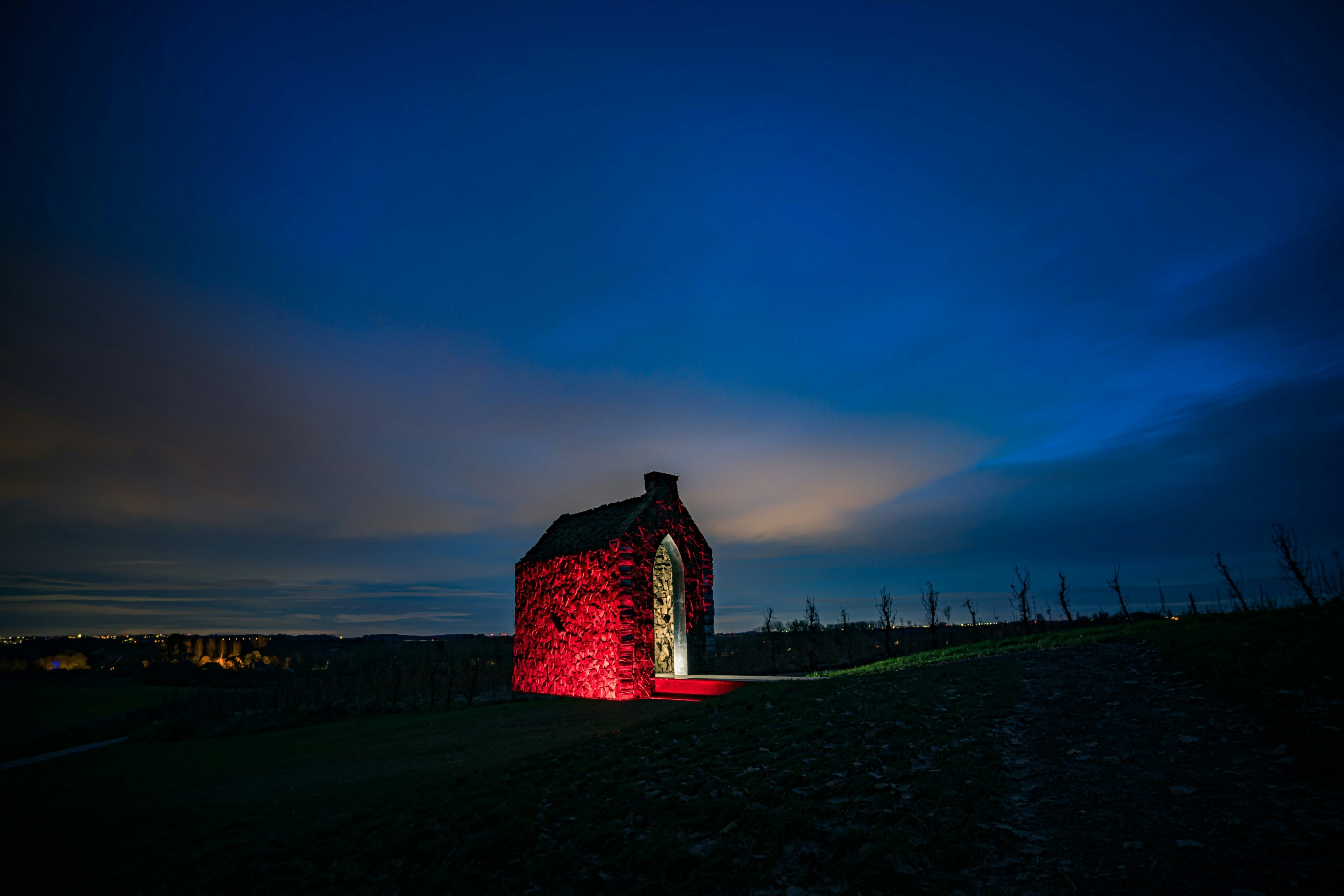 Crimson doorway of a lone dusk chapel beneath a cobalt sky