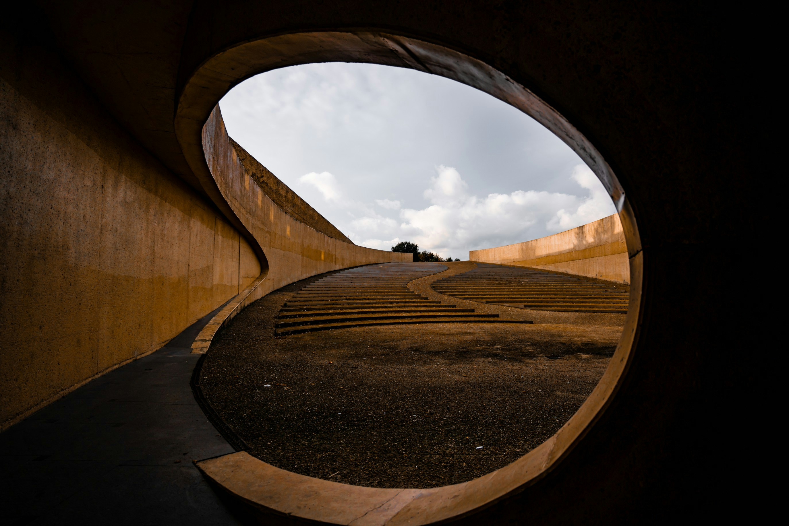Oculus Exit: A Distant Car Framed by a Circular Concrete Arc