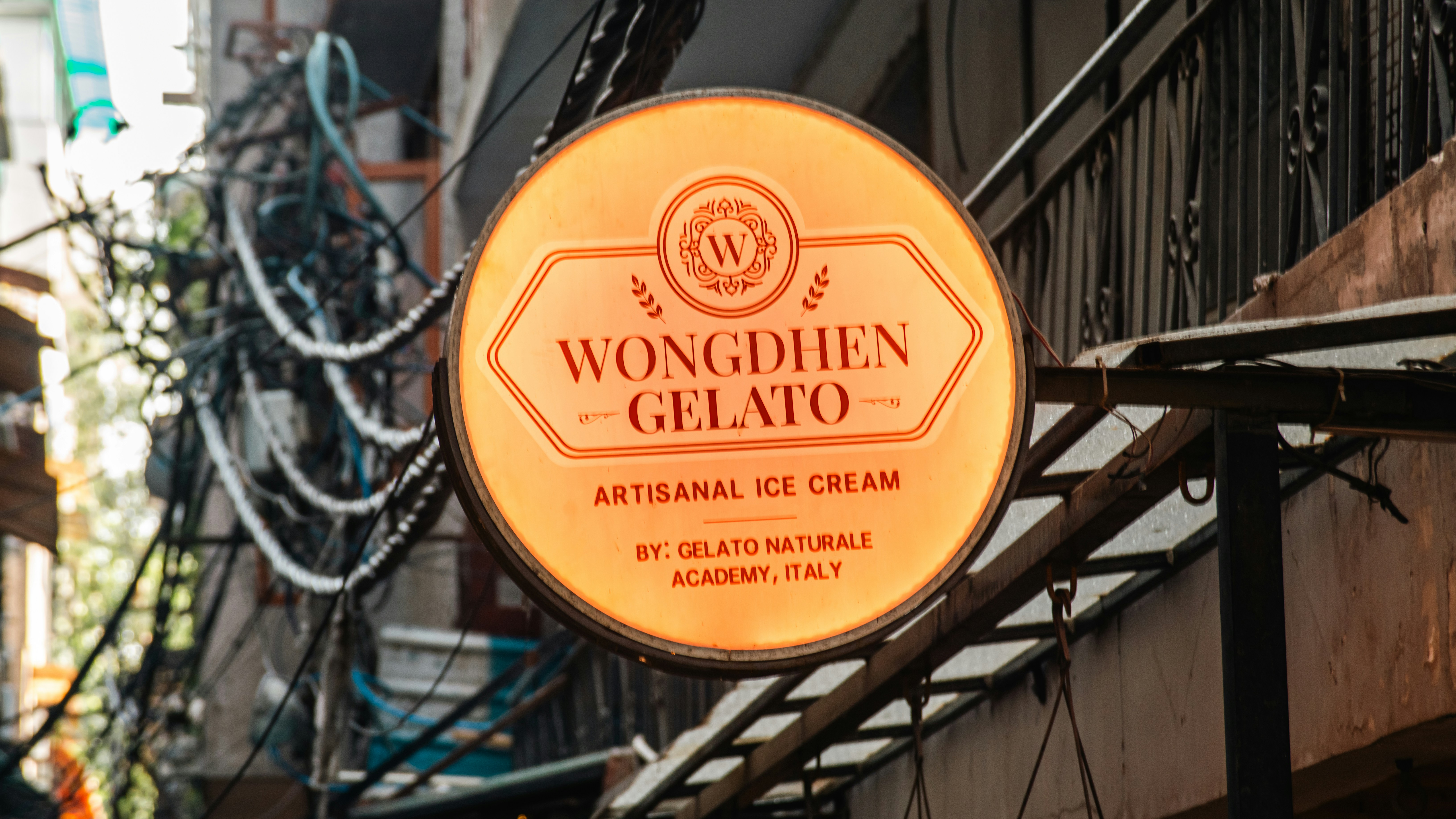 Orange Gelato Sign Looms Over a Cluttered Alley of Cables