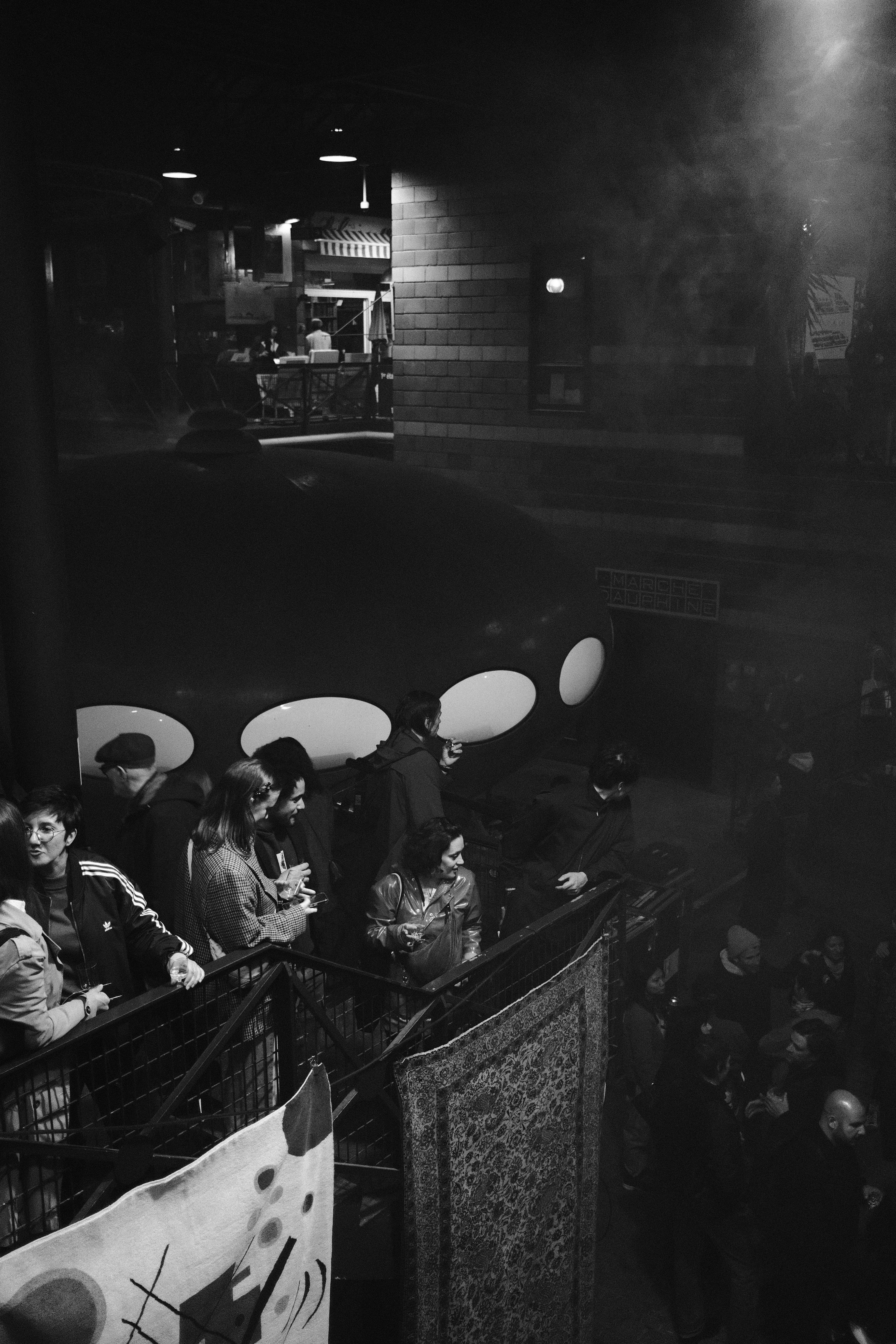 Monochrome Terrace: Faces Gather Along a Dim Cafe Balcony