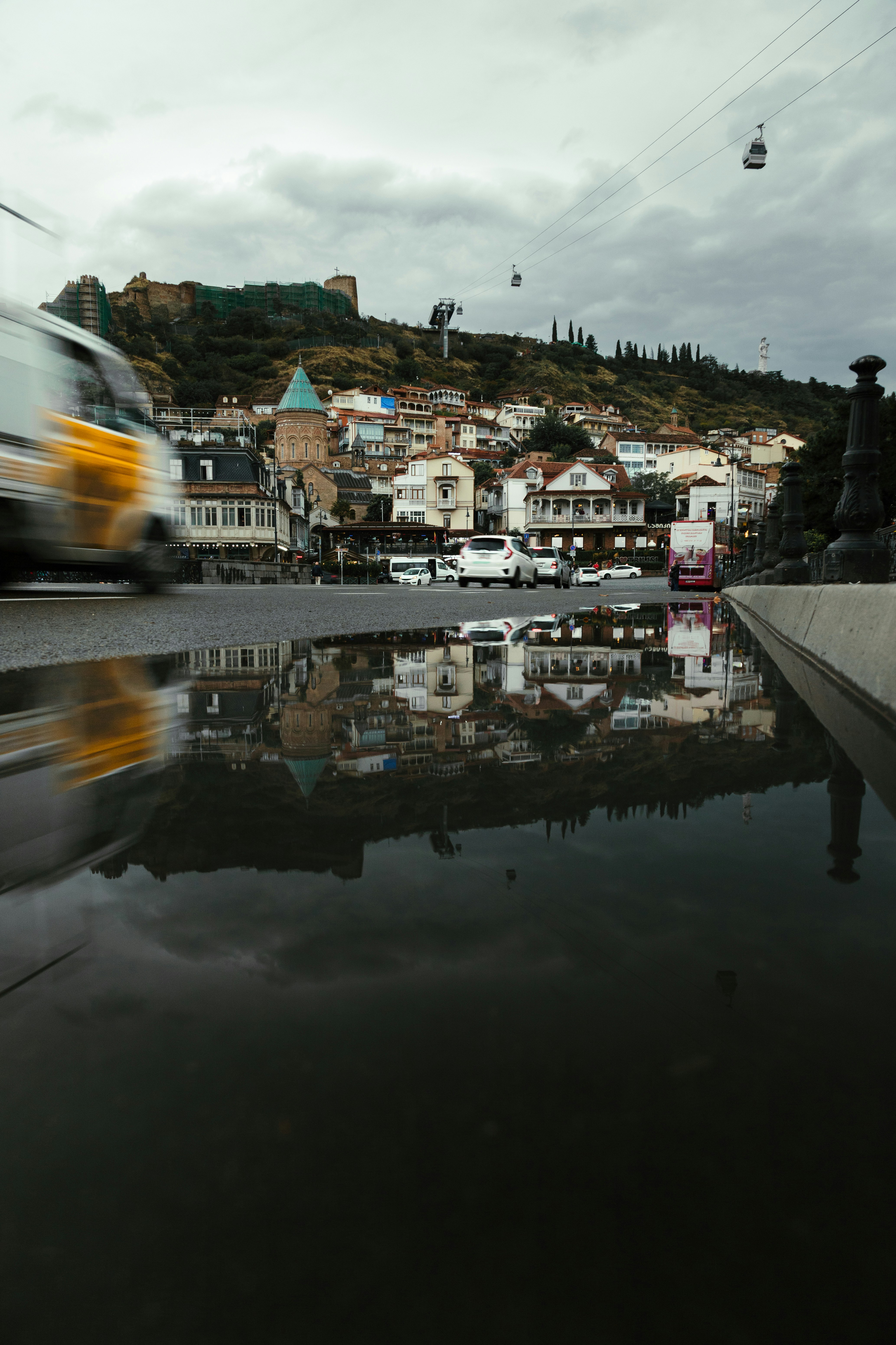 Cable Cars Above, Puddle-Mirror City: A Hillside Town in Motion