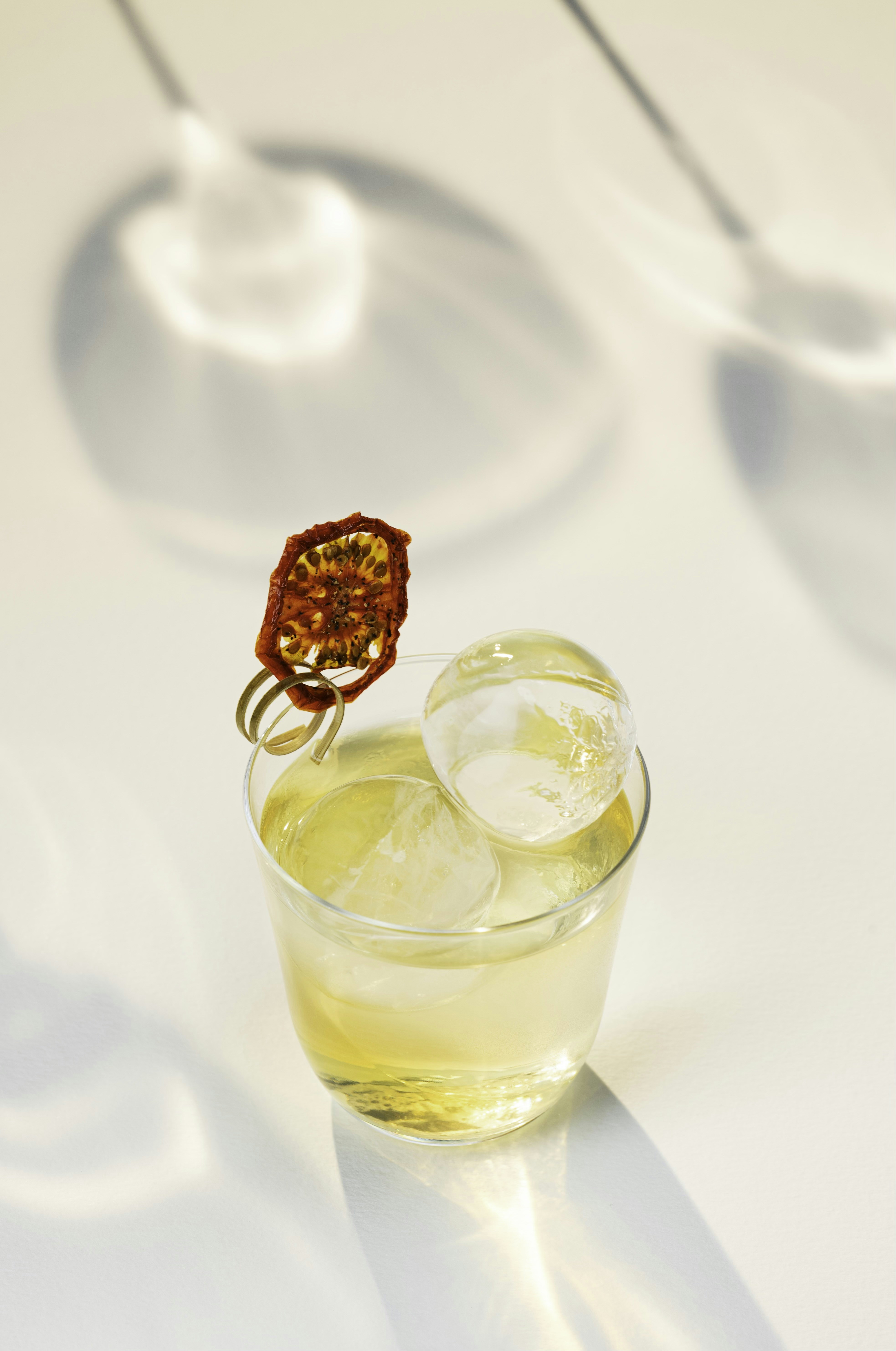 A clear cocktail with ice and dried tomato garnish.