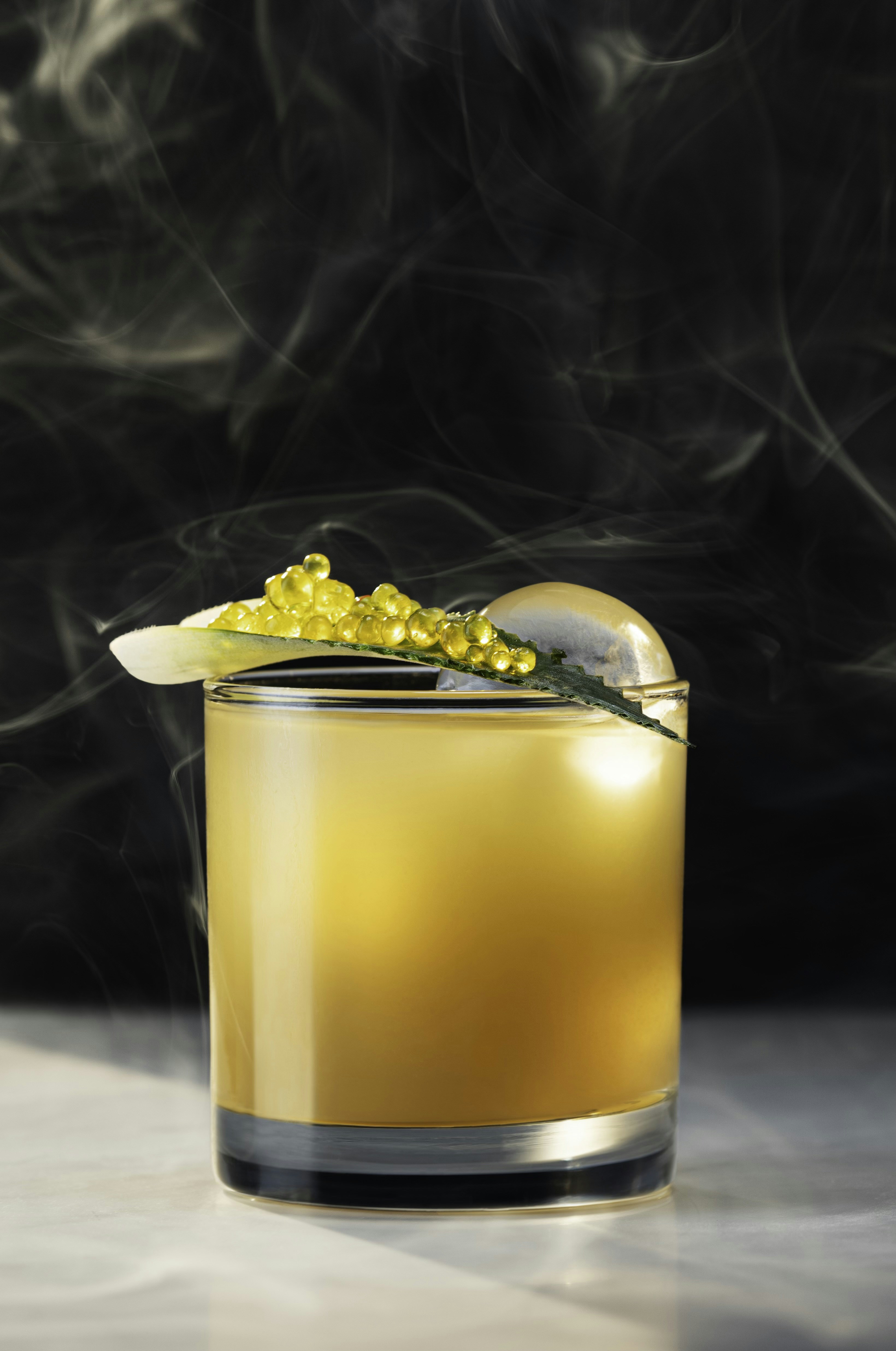 A smoky cocktail with yellow pearls and garnish