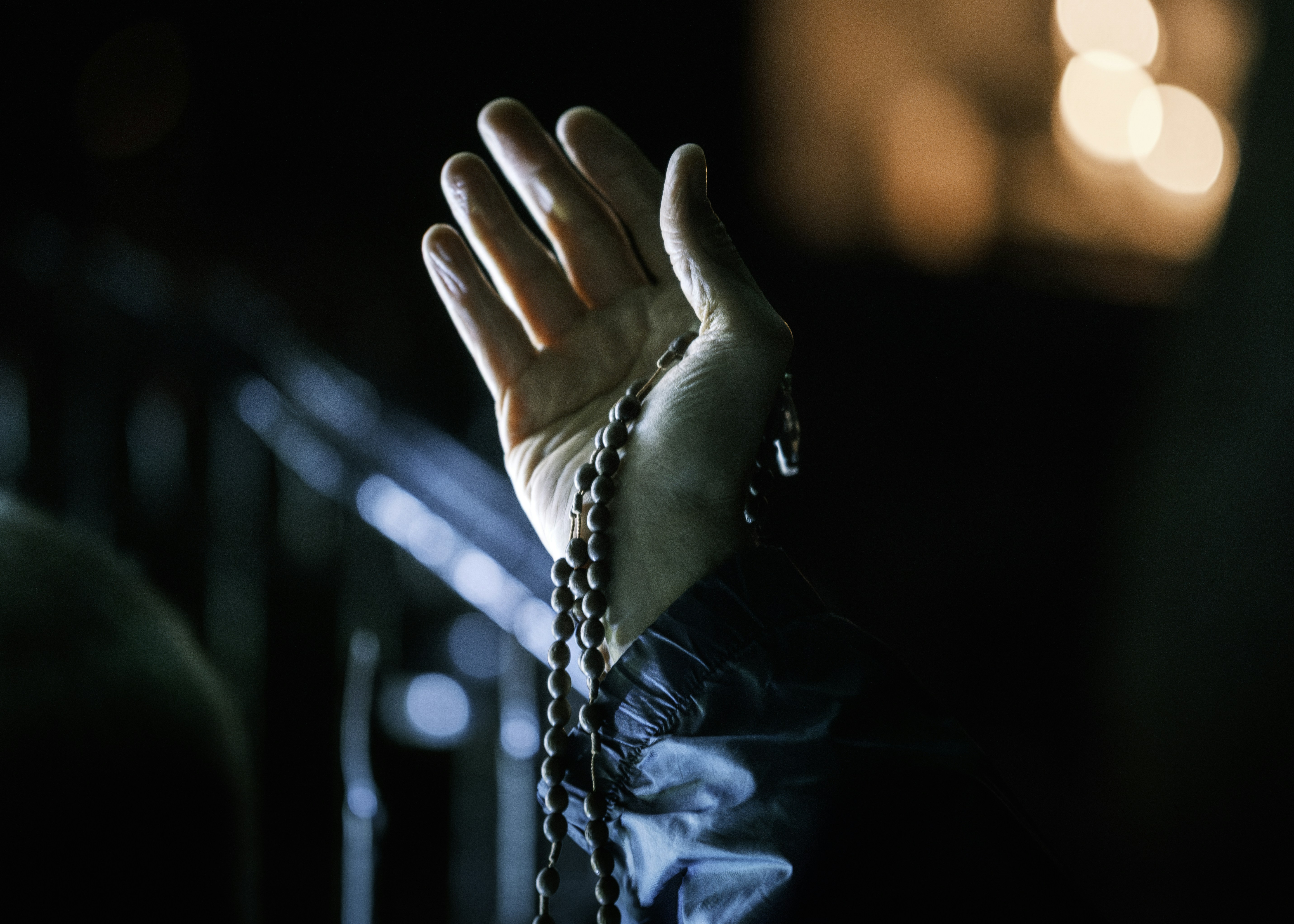Beads in Neon Night: A Raised Hand Amid Warm Bokeh