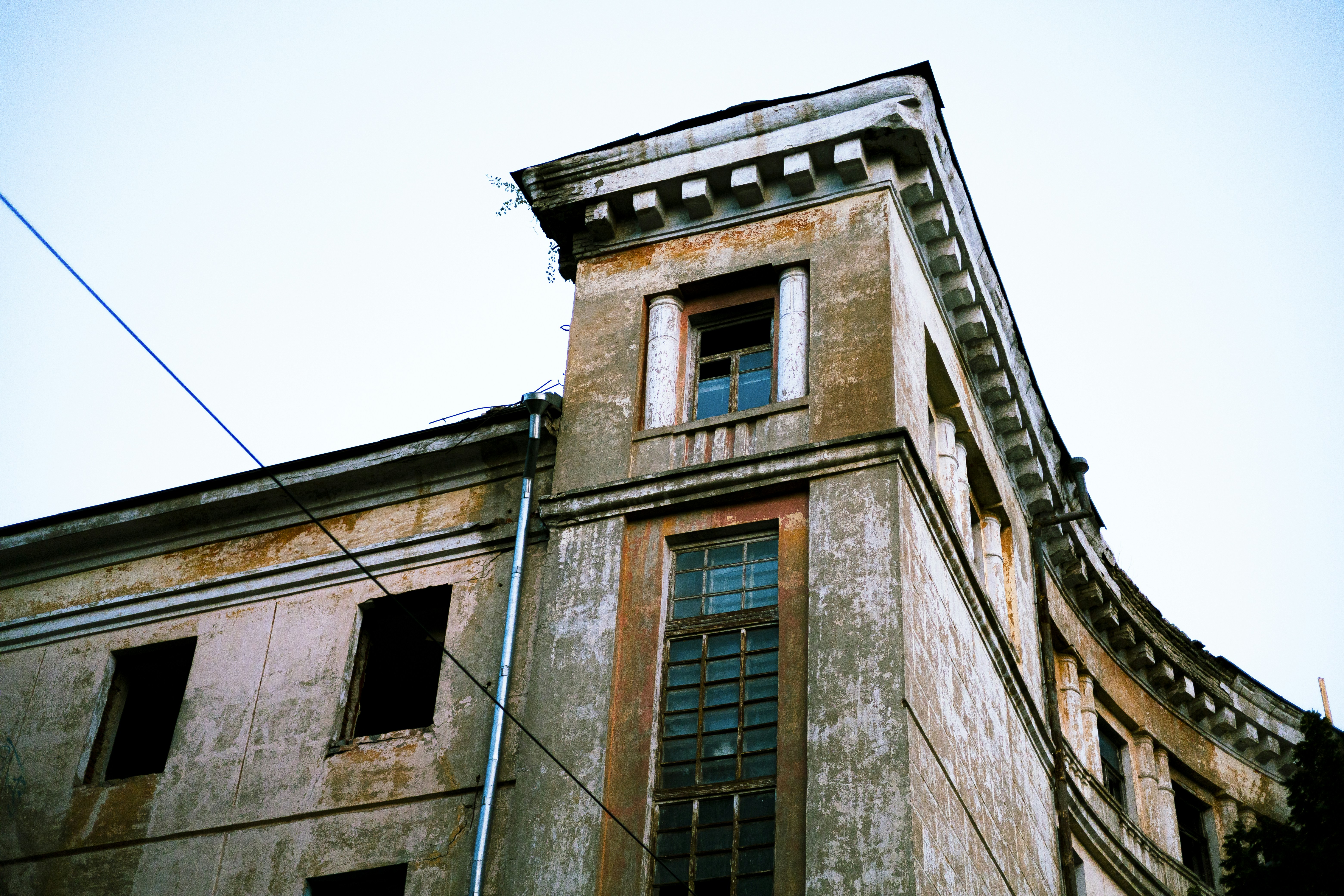 A close-up of an abandoned building reveals the haunting beauty of decay and time. The weathered facade, cracked plaster, and empty windows speak of a forgotten past once filled with life. The warm tones of aged stone contrast against the pale sky, emphasizing the intricate classical design now fading into ruin. Perfect for those who appreciate architectural history, urban exploration, and the poetic elegance of decay.
