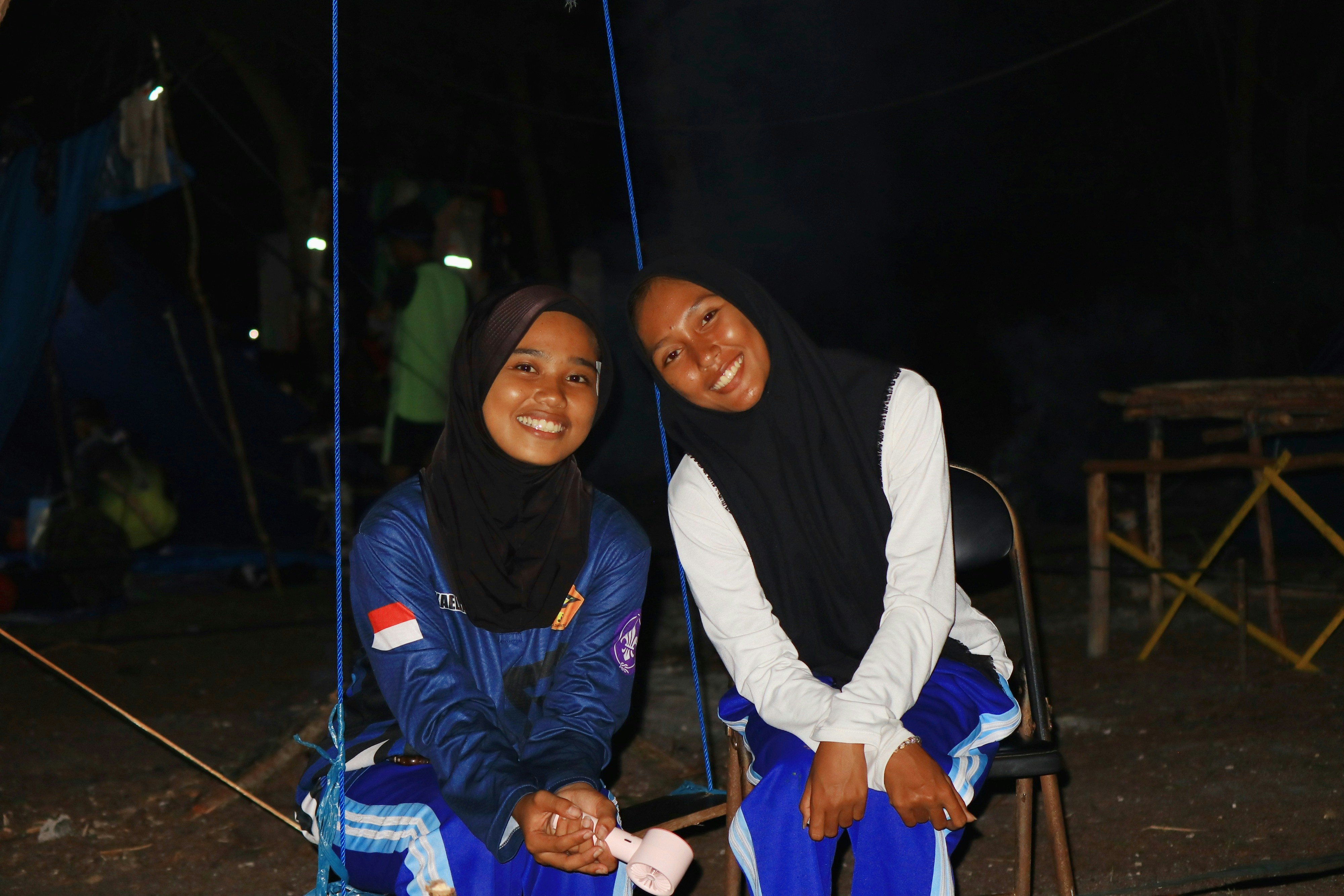 Night Campside Smiles: Duo in Blue Uniforms Beneath Quiet Lanterns