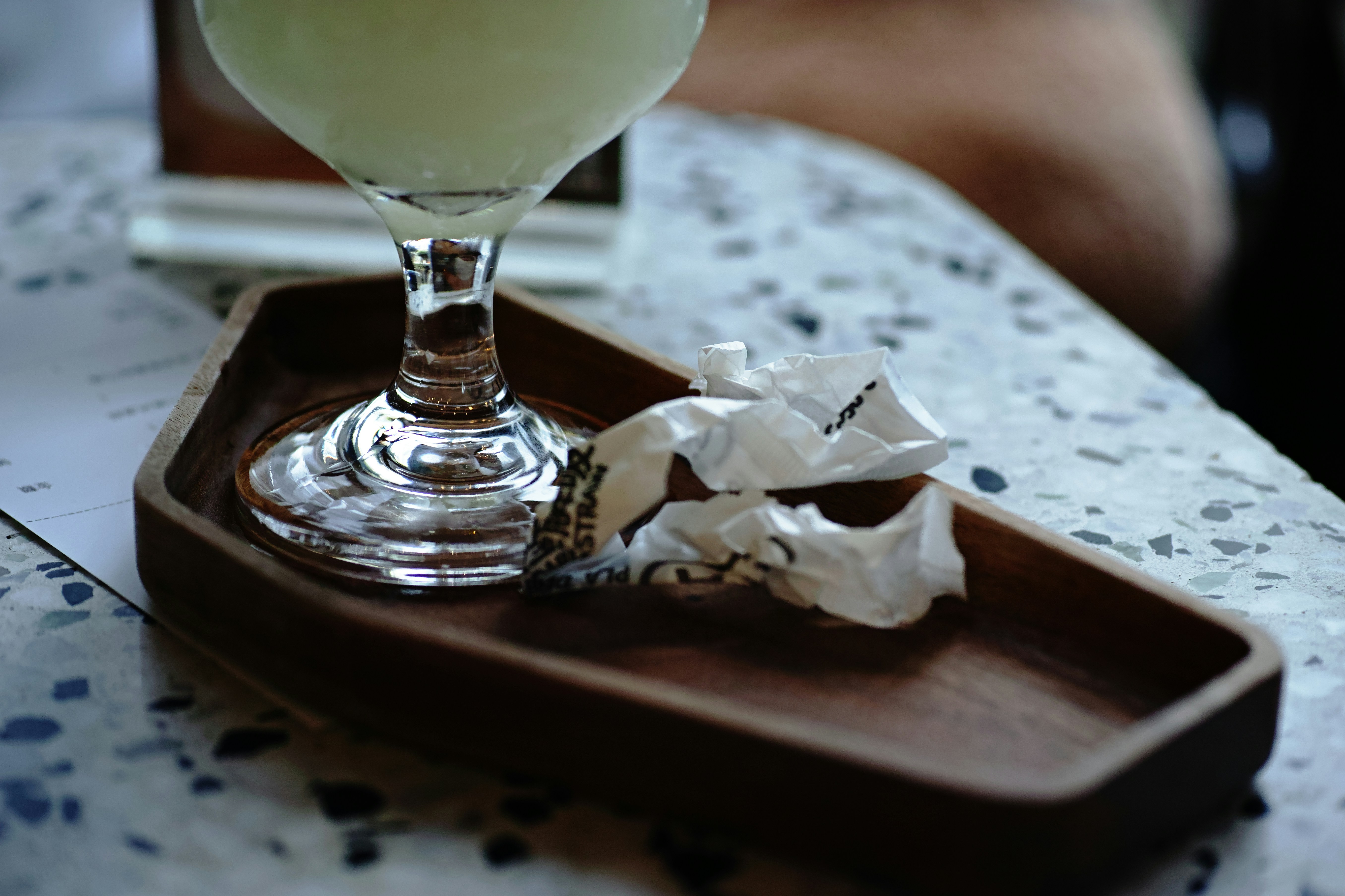 Green cocktail on a wooden tray with crumpled napkin, set on a speckled tabletop.