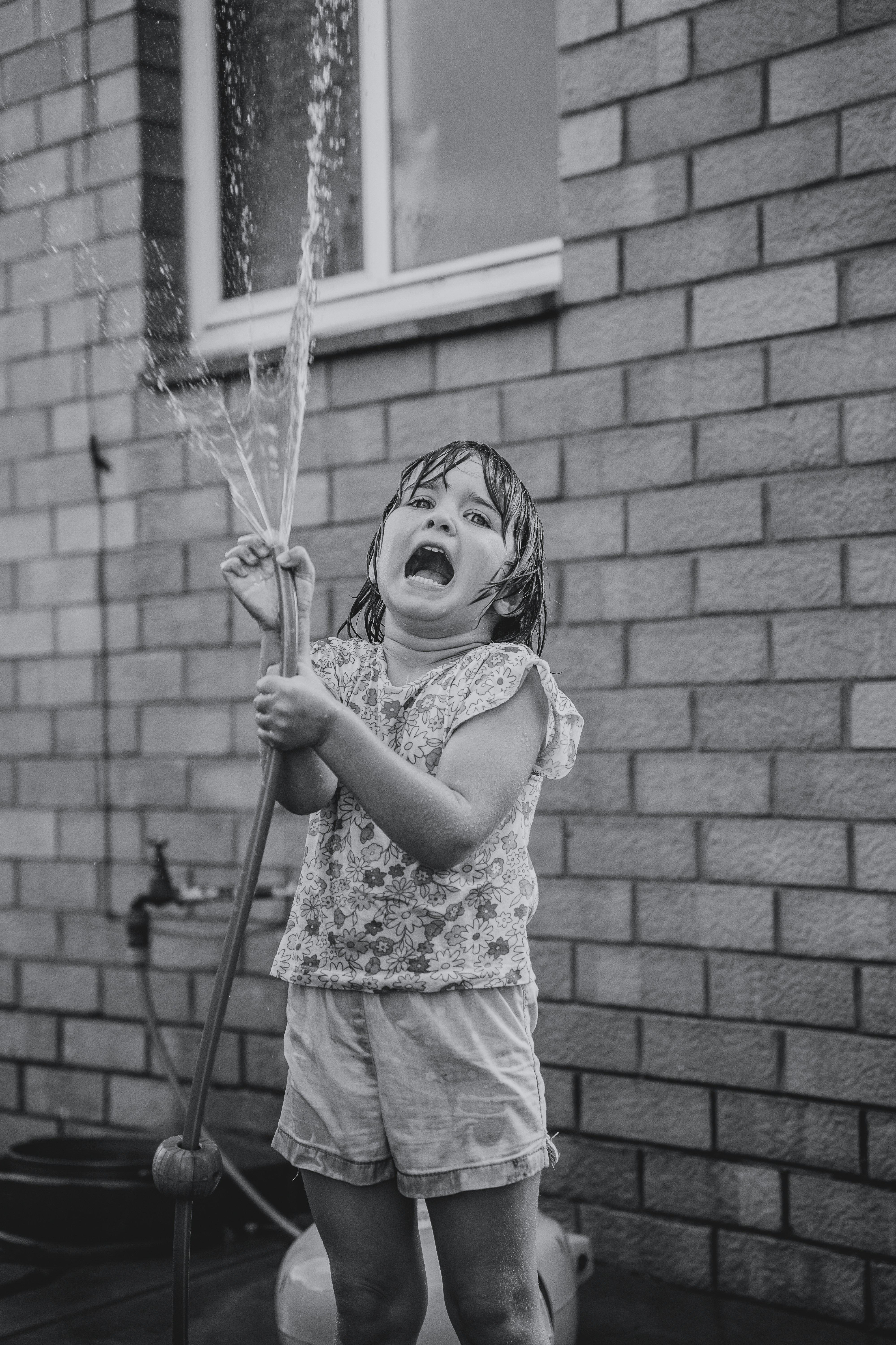 Joy in the Spray: A girl's laughter against a brick backdrop