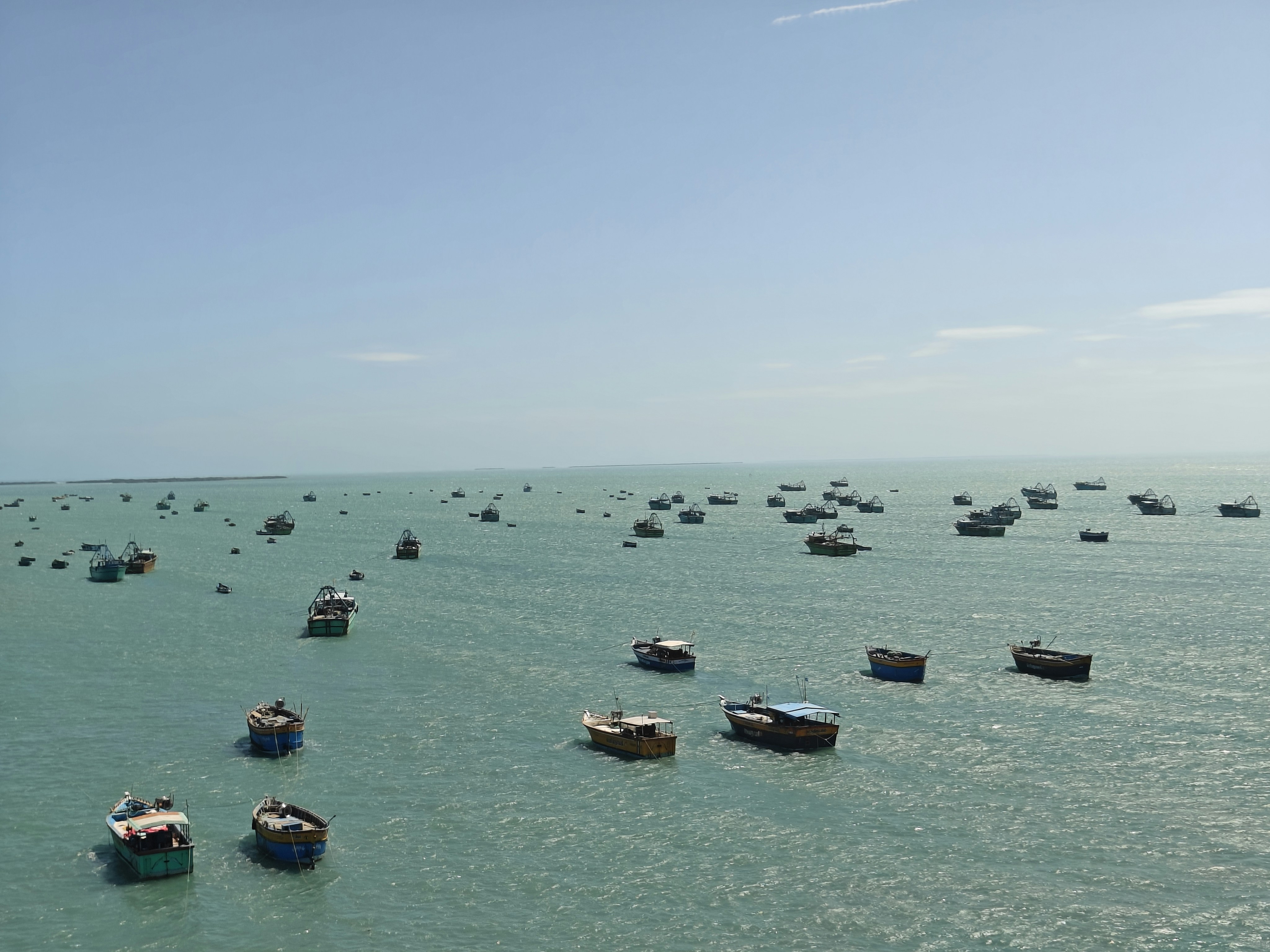 Many small boats float on the calm blue ocean.