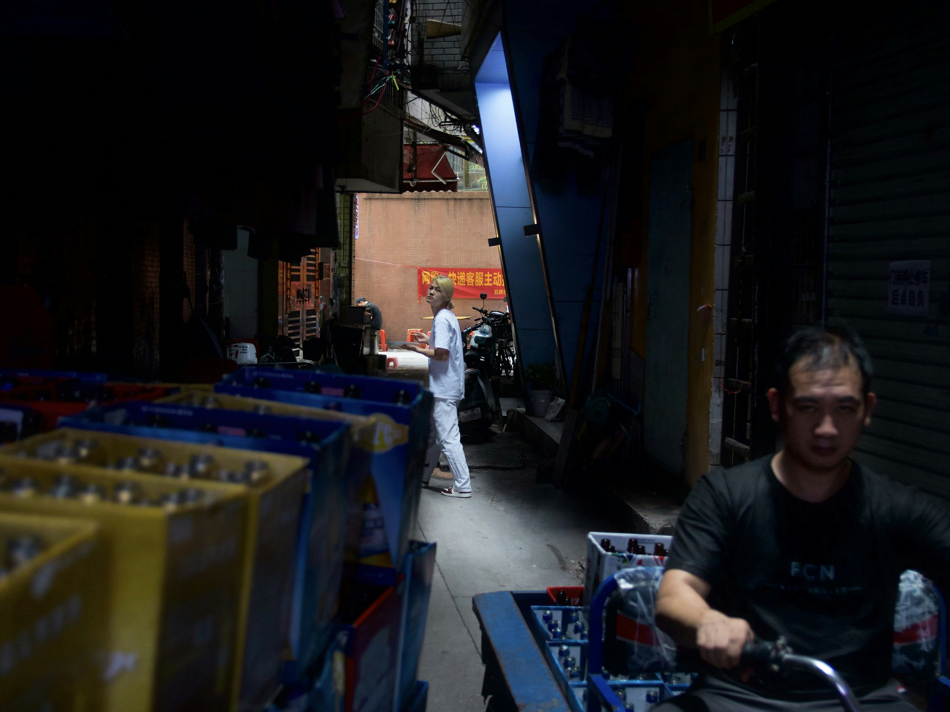 Light at the End of the Alley: A White-Clad Figure in a Crate-Framed Market
